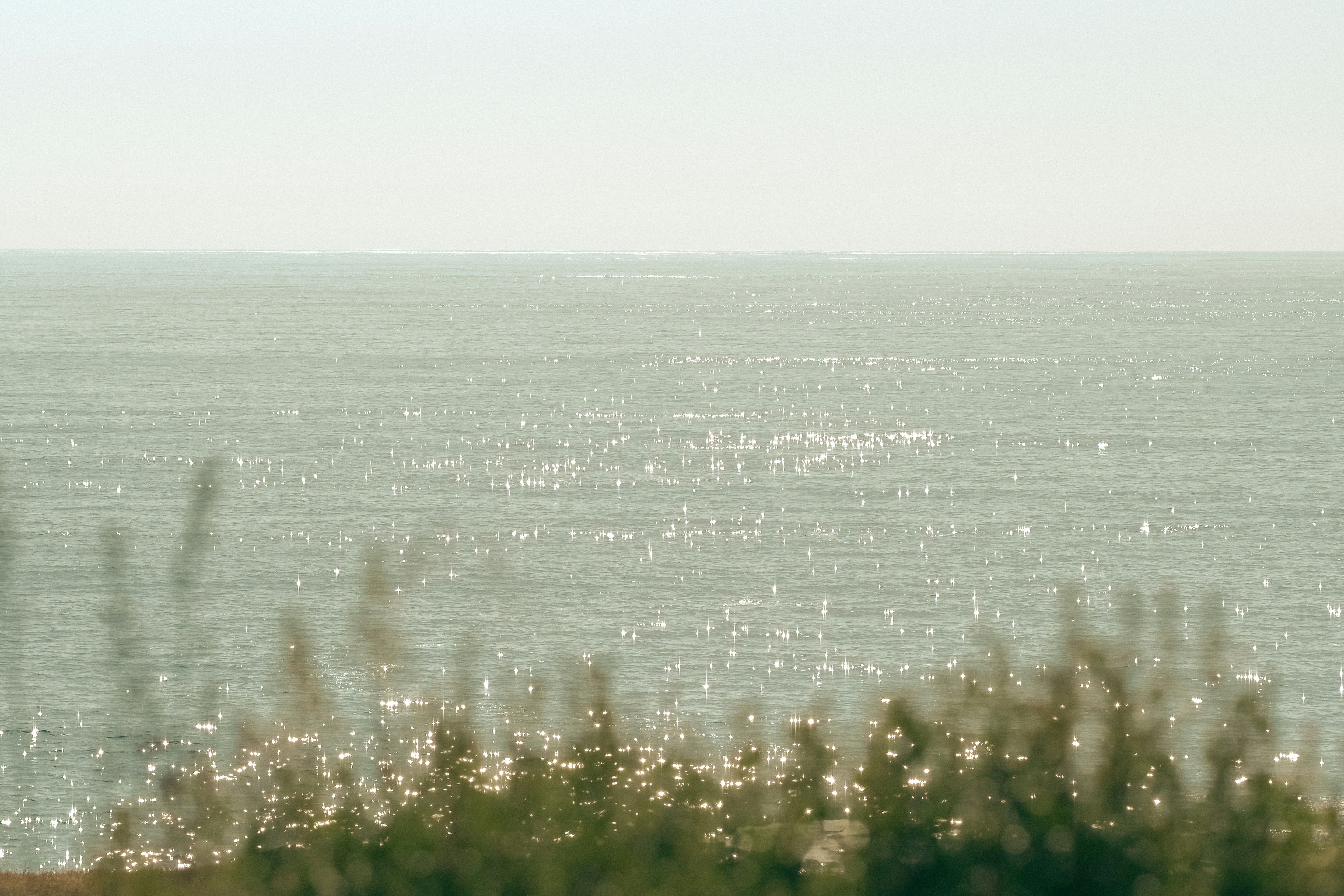 Shimmering Sea: Sunlit Crest Beyond a Hazy Horizon
