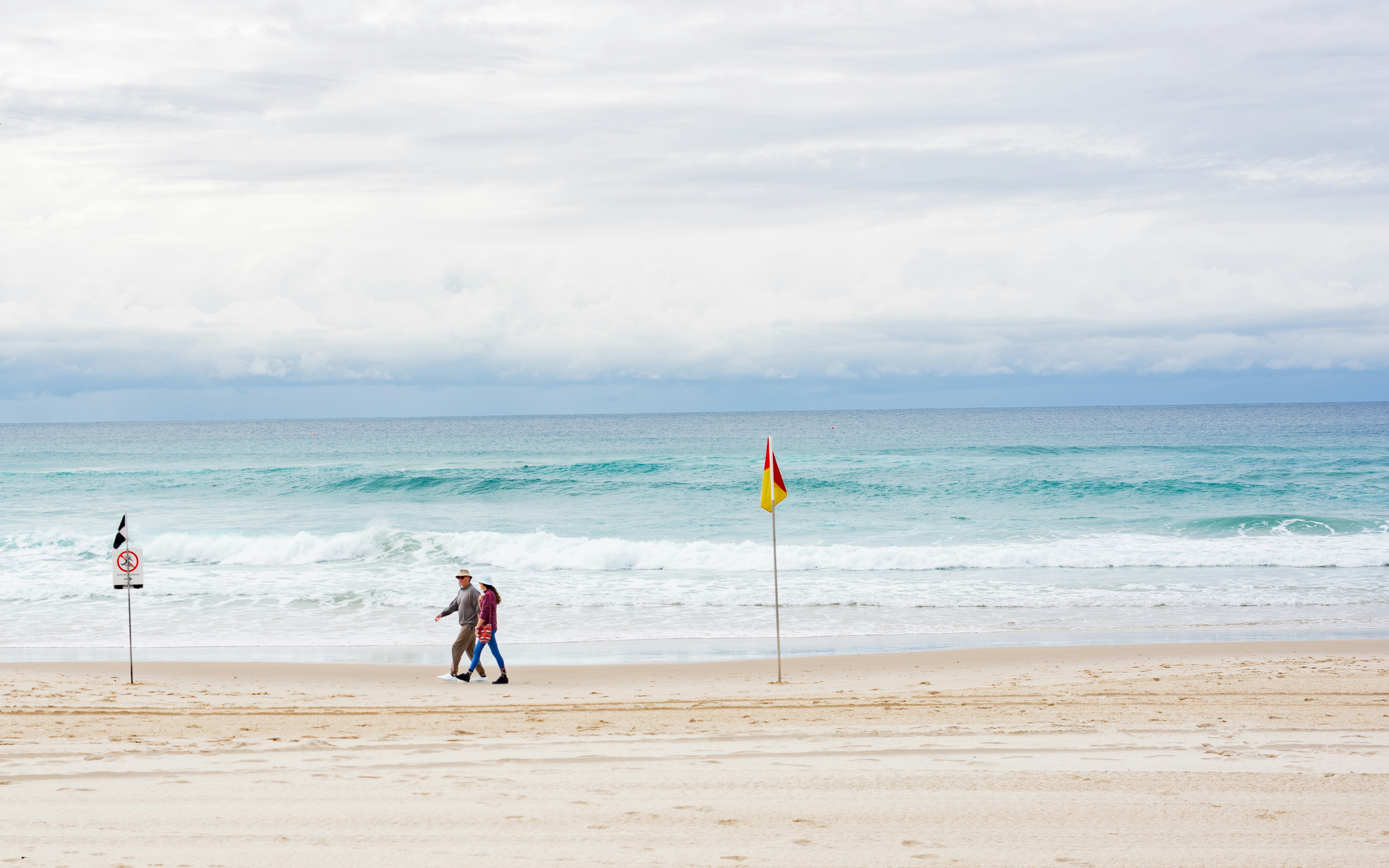 Two silhouettes stroll the sunlit beach under a calm horizon