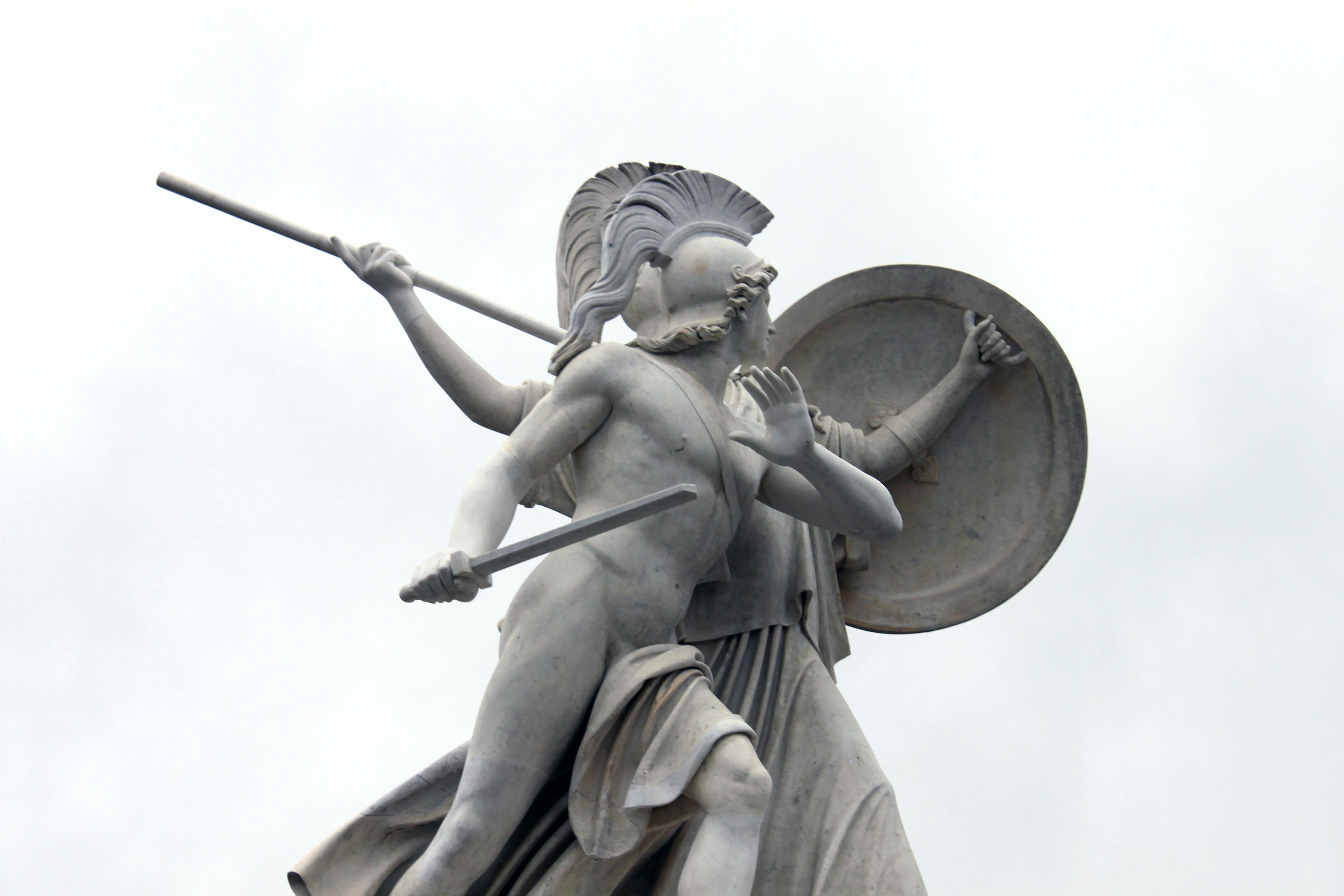 Statues of two warriors in dynamic pose, one wielding a spear and the other with a shield, sculpted sculpture against a pale sky.