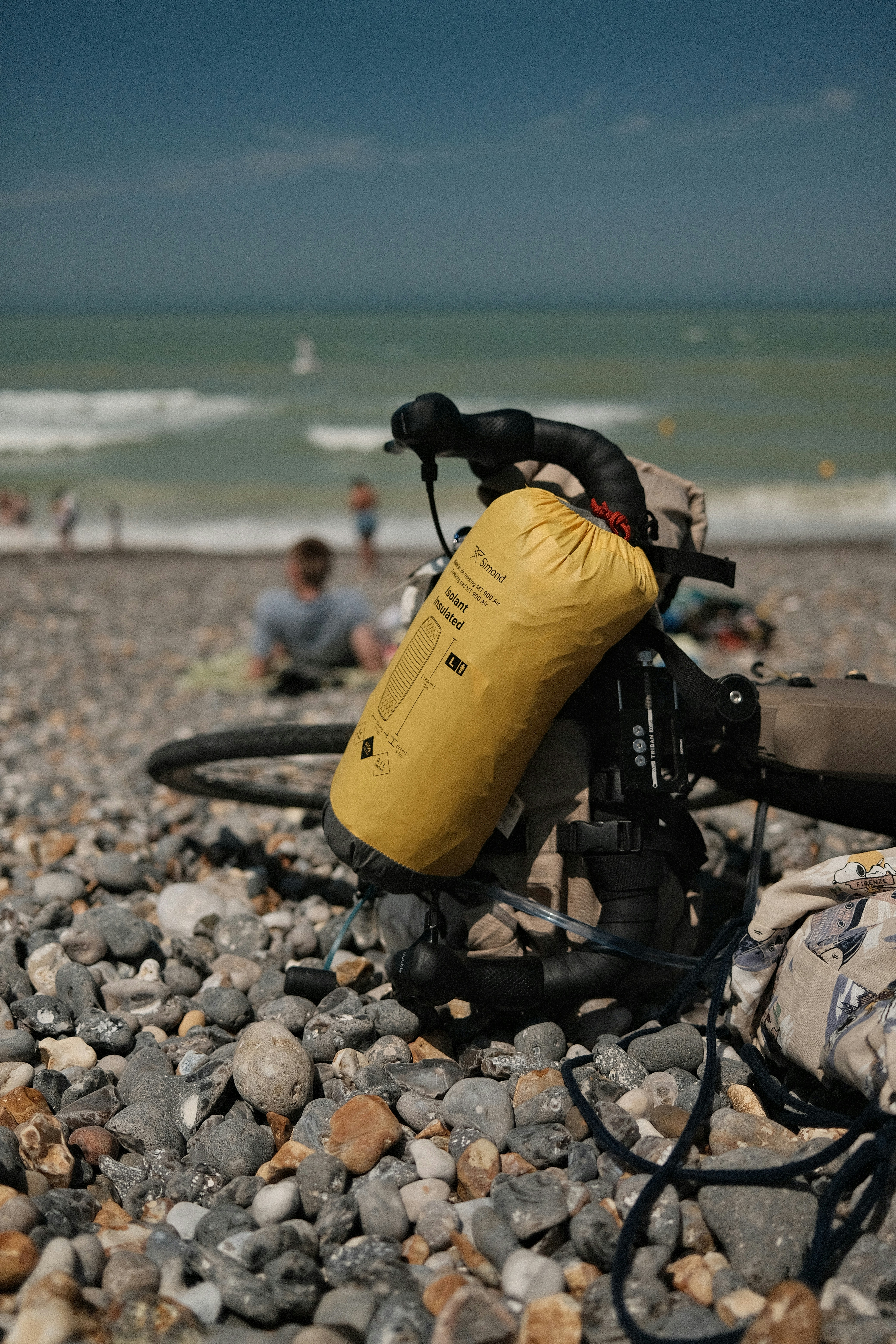 Yellow Pack on the Beach: A Gear-Loaded Bicycle Resting by Pebbles