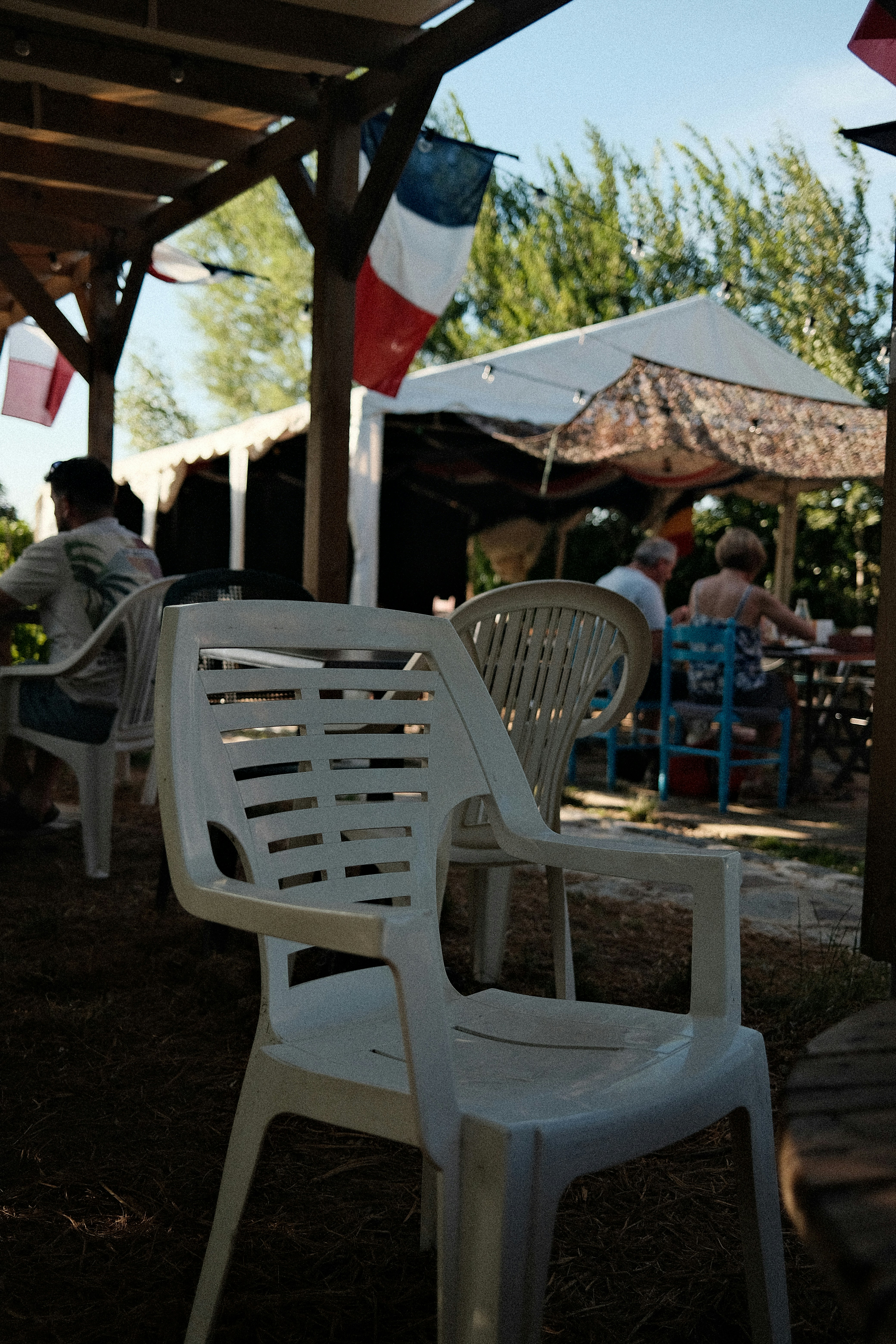 Empty chair under a shaded canopy with festive flags and social activity in the background