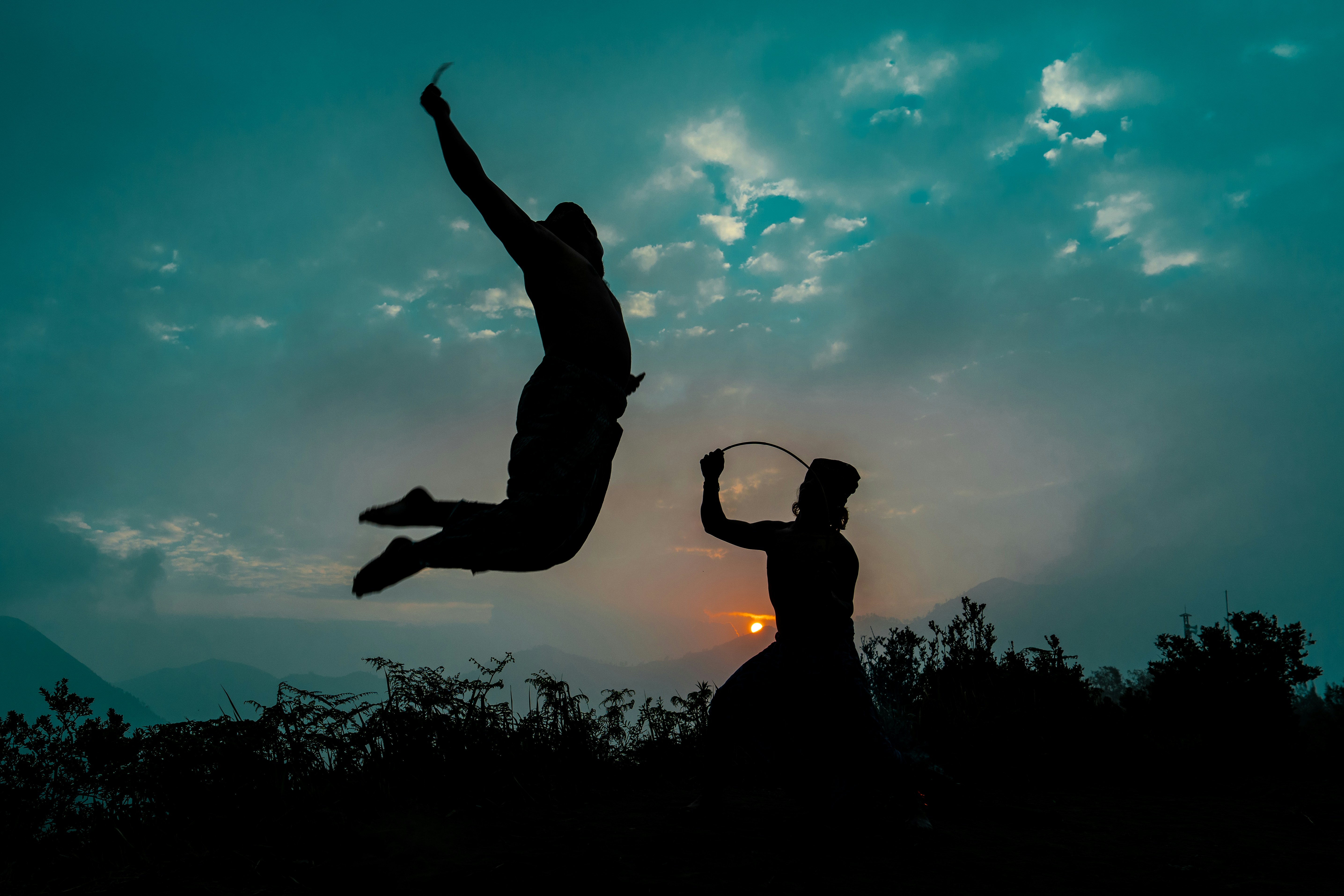 Silhouetted Jump: Two Figures Soar Against a Teal Sunset