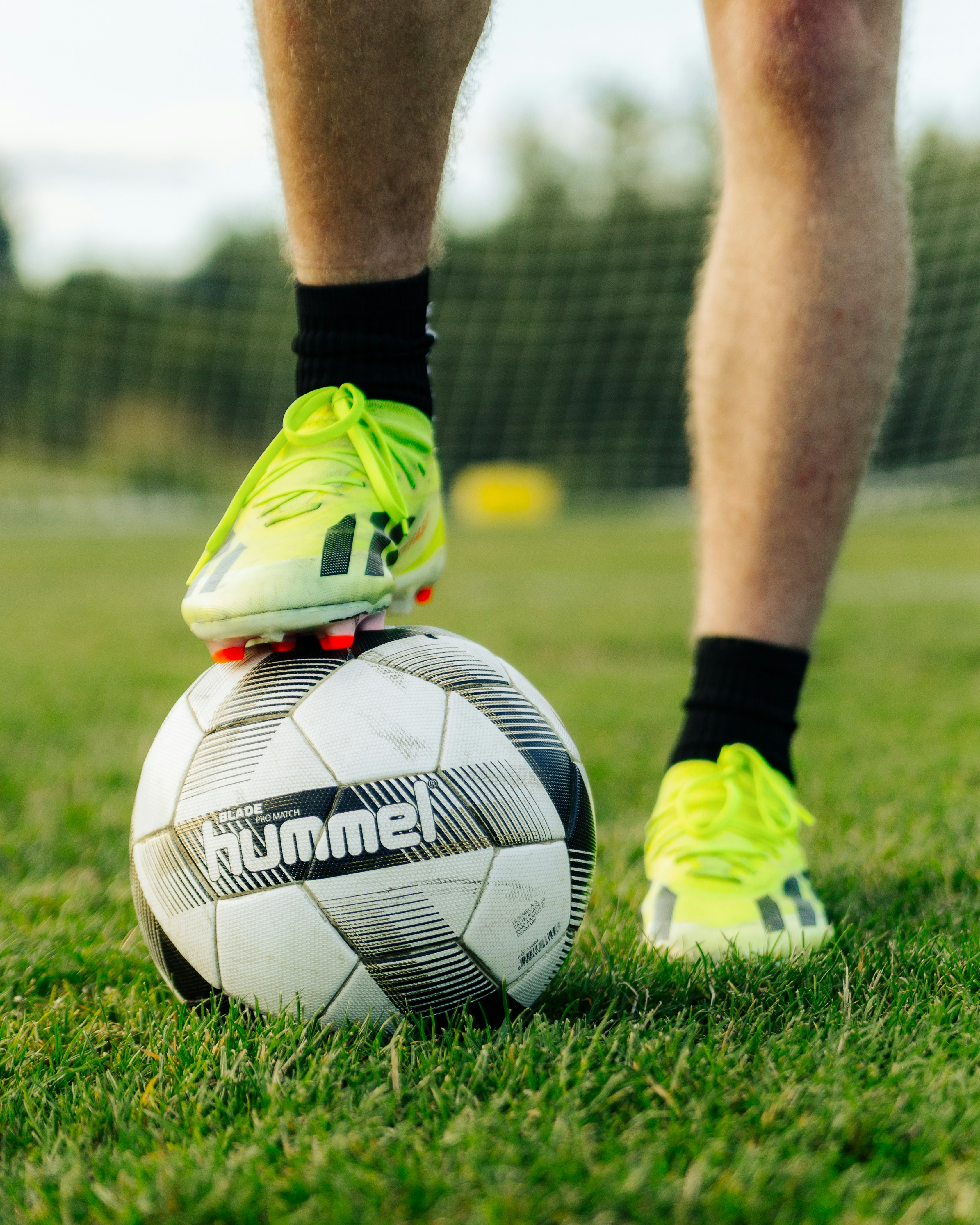 Soccer cleats rest on a ball during training on a grassy field, with a focus on the footwear and foot positioning.