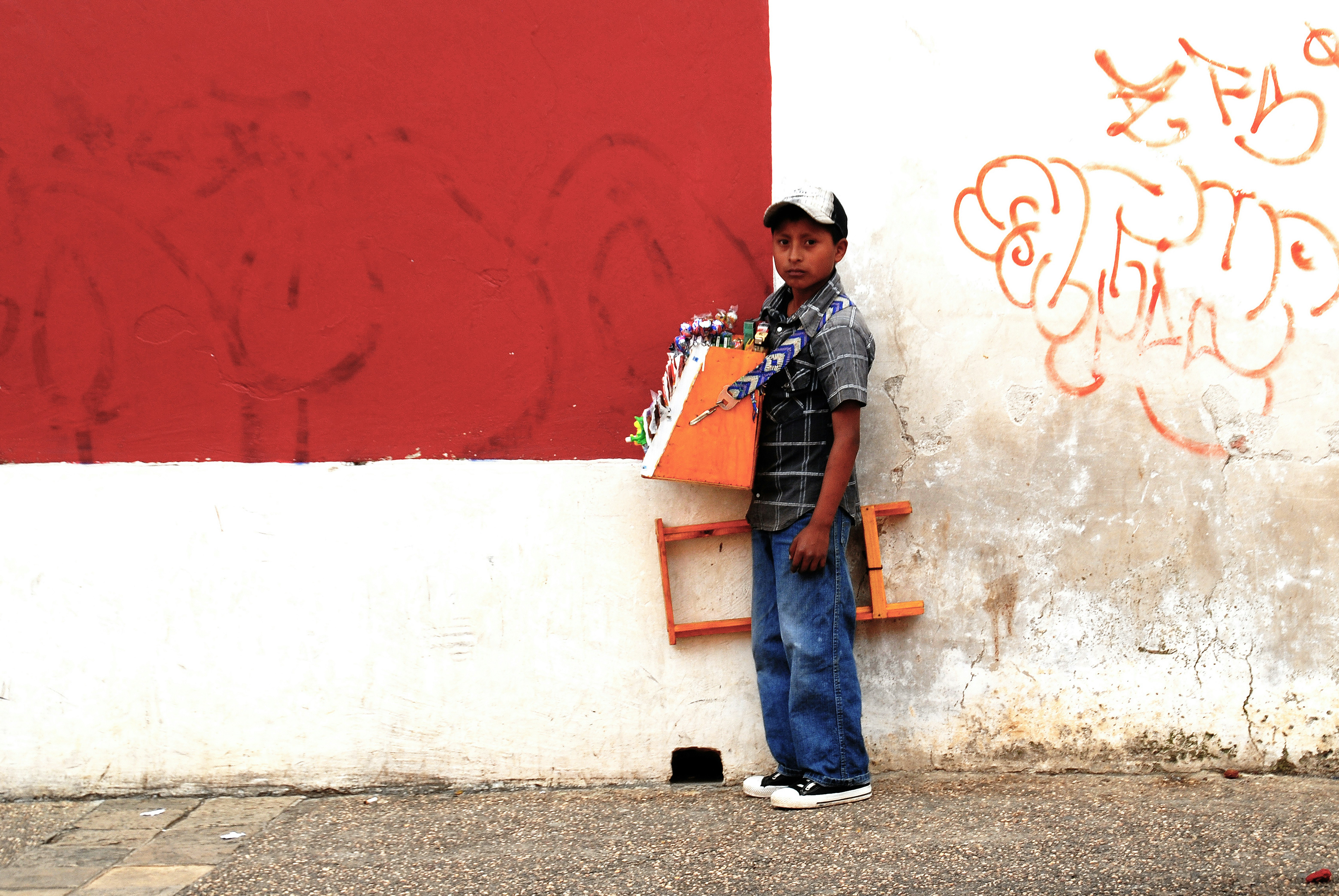 Boy with a wooden cart of bottles leans against a graffiti-streaked wall