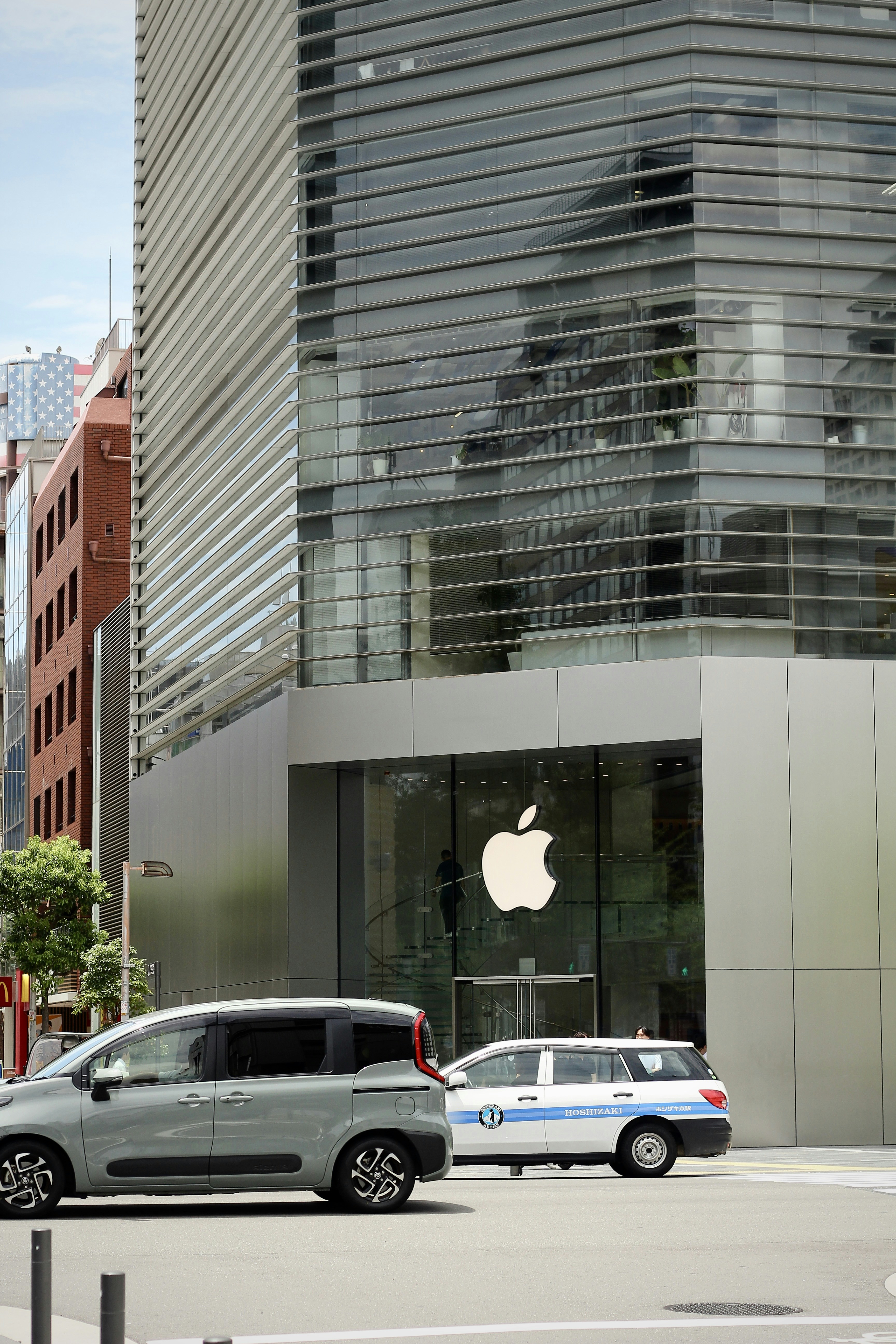 Apple flagship on a city street: glass tower and parked vehicles