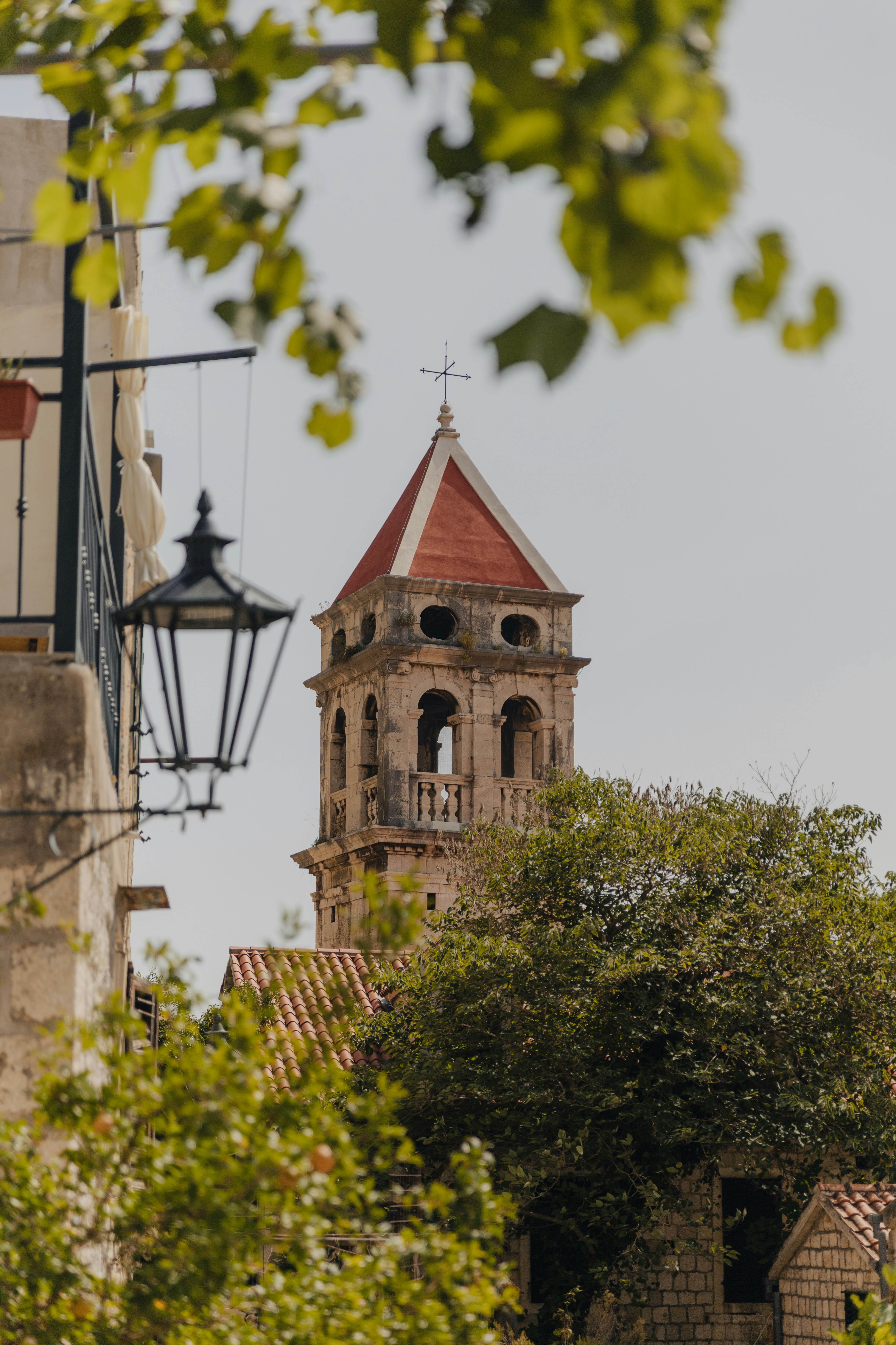 Towering Bell Tower with Red-Tiled Roof Emerges Through Verdant Canopy