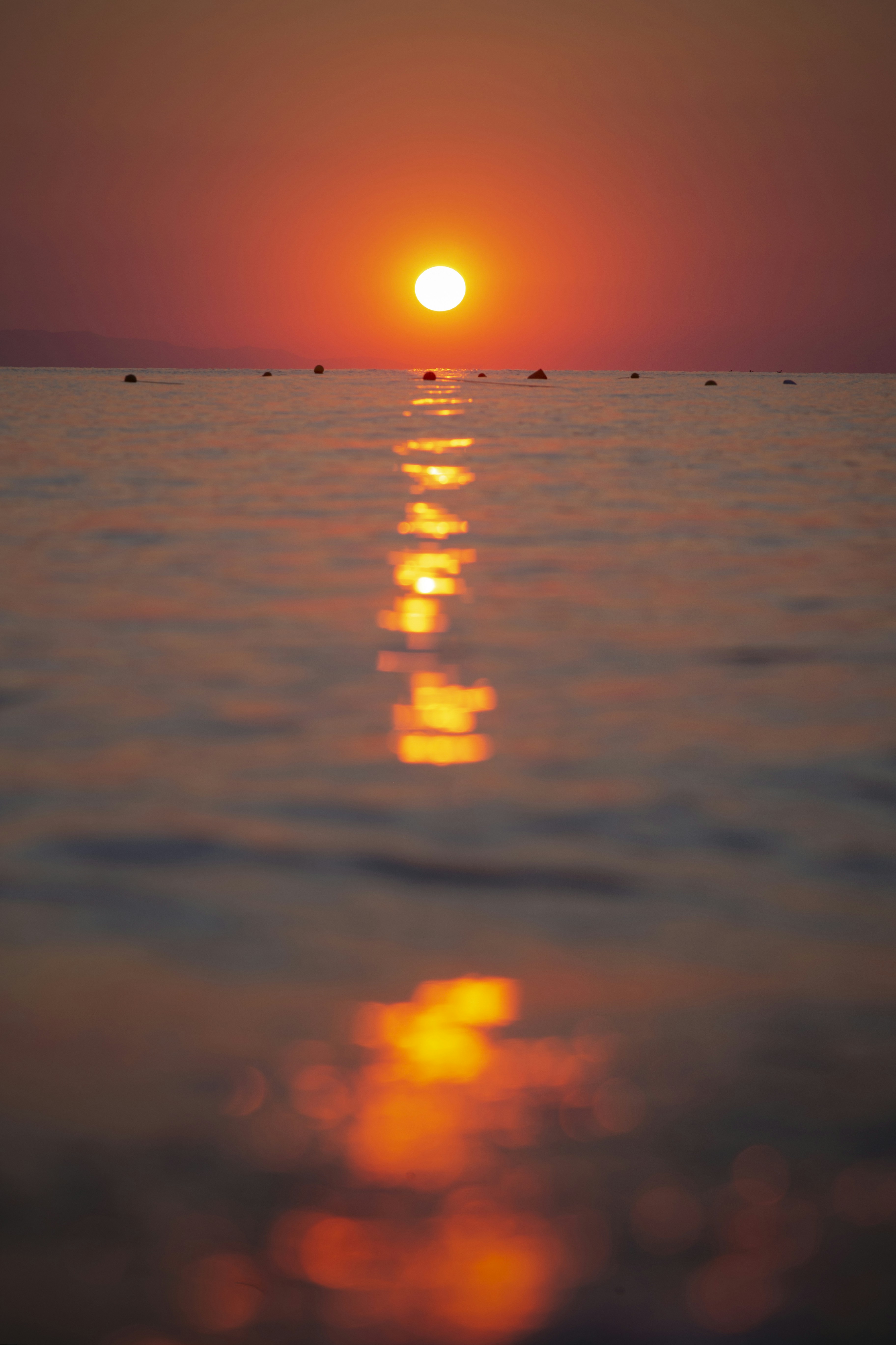 Vibrant sunset over calm water with a bright sun and a glowing reflection stretching toward the foreground; a tranquil seascape with distant rocks along the horizon. (photograph) .