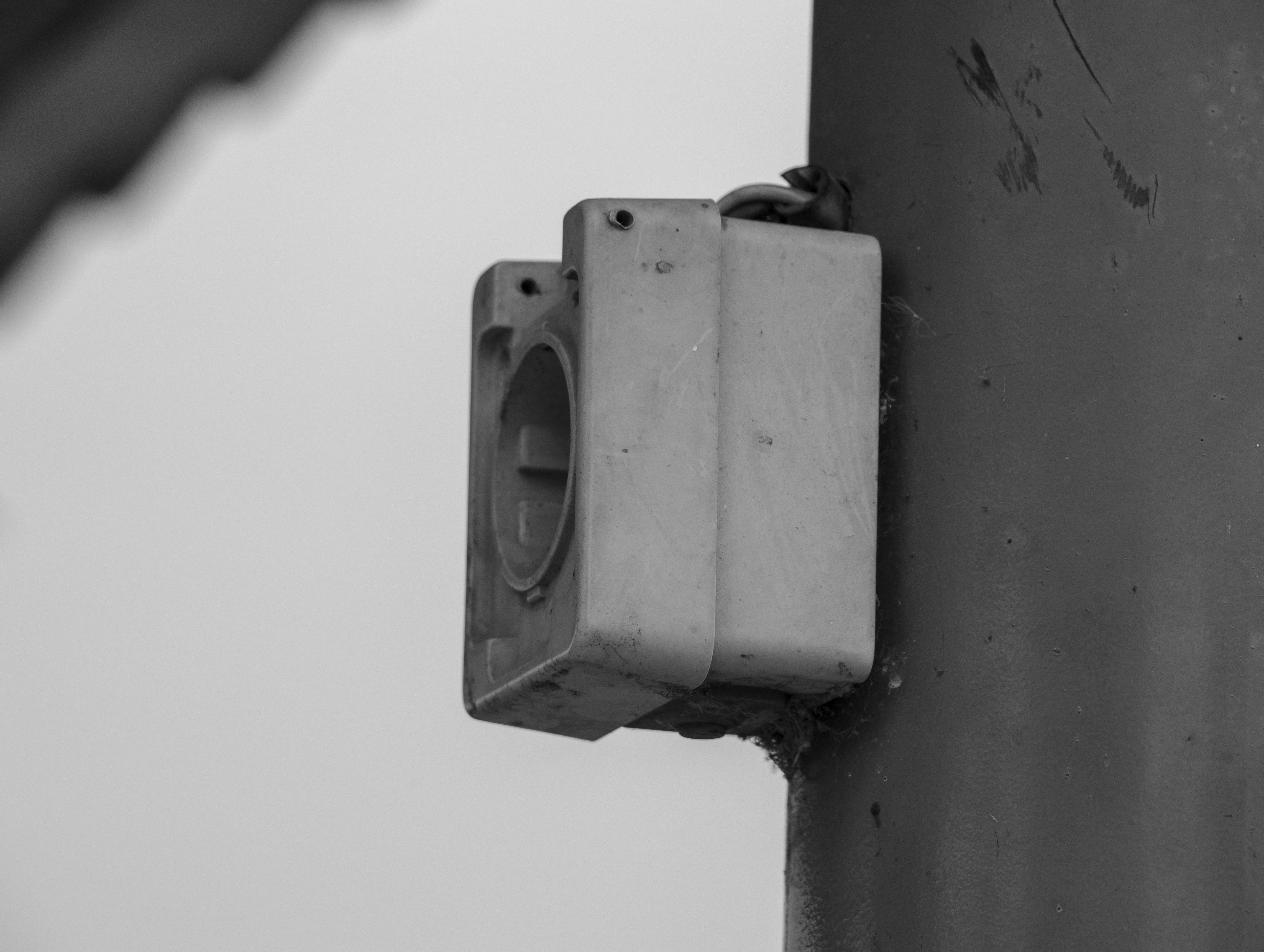 Close-up of a small, weathered metal latch attached to a vertical steel beam; grayscale emphasis on texture and industrial minimalism.