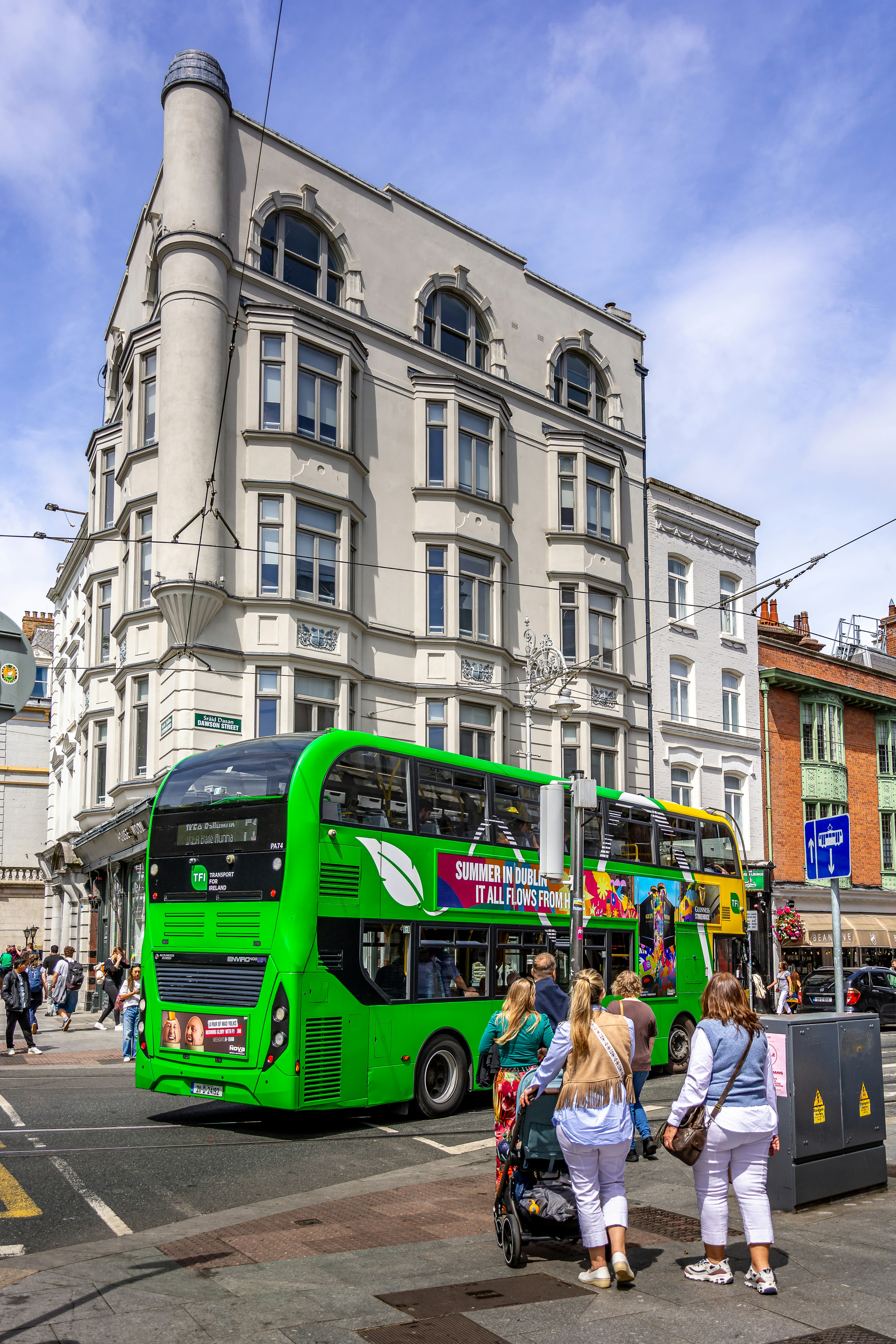 Green double-decker at a sunlit city corner