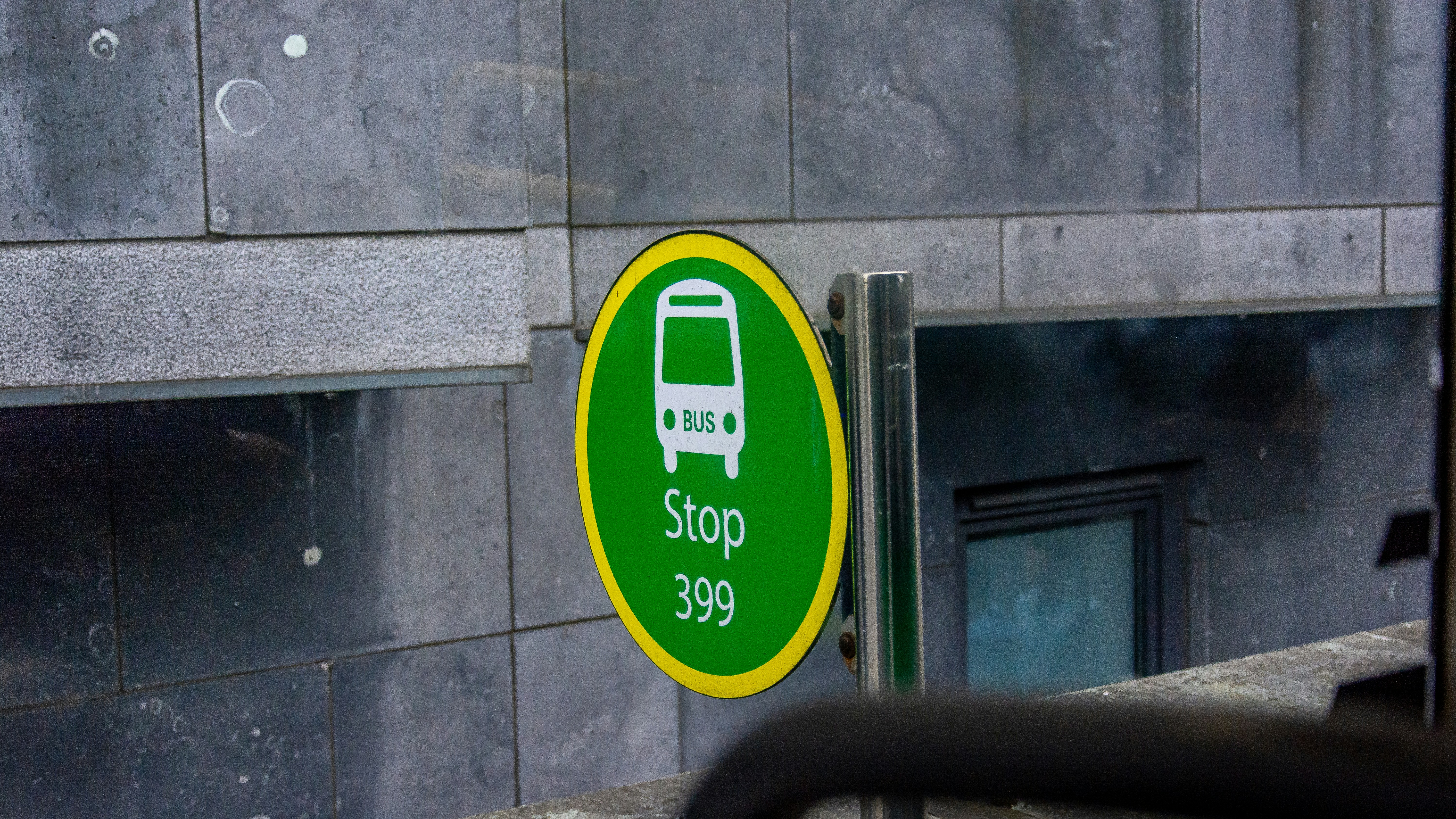 Green Bus Stop Sign Emerges from Urban Facade
