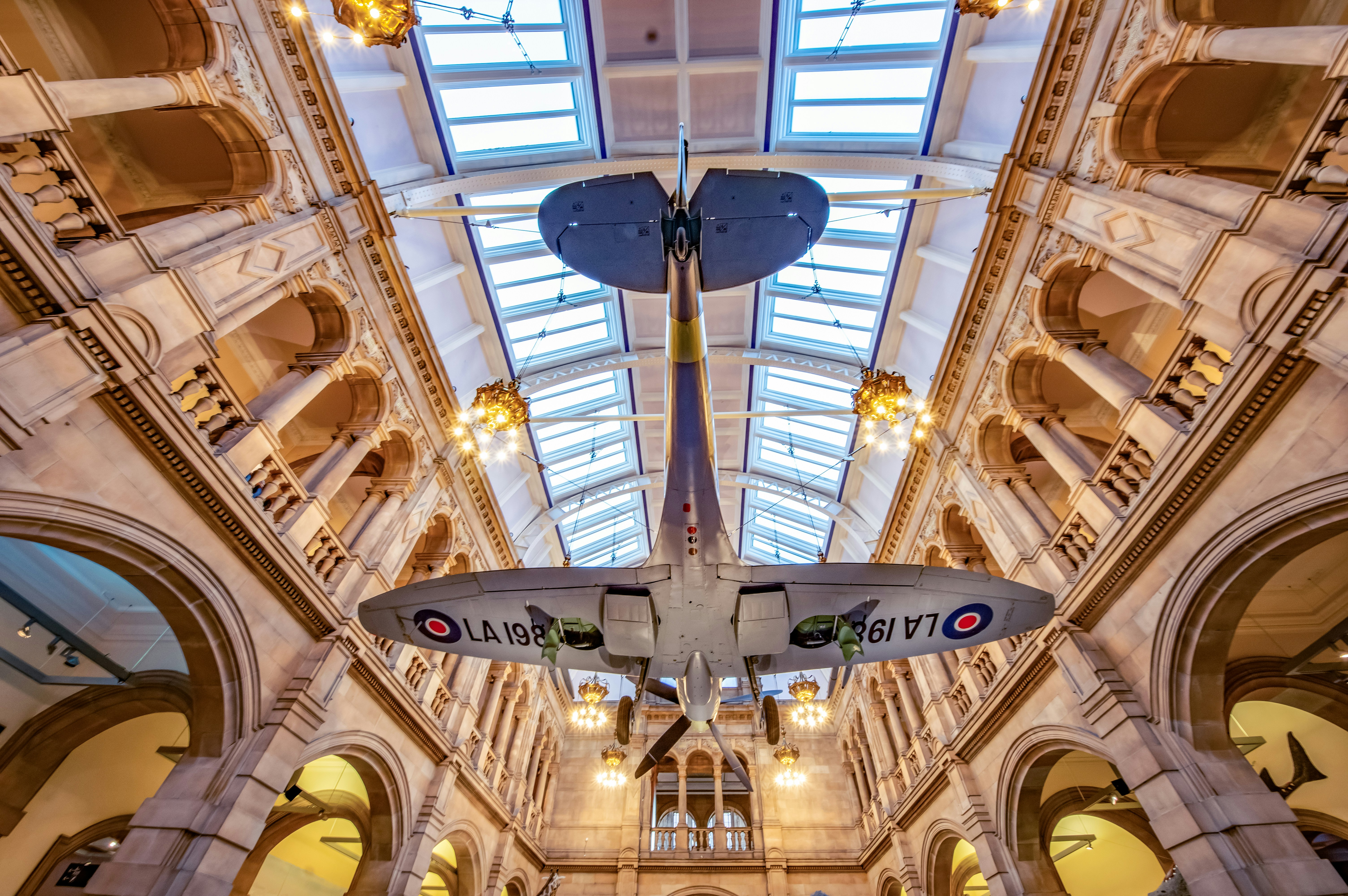 Historic aircraft suspended in a grand, vaulted hall with gilded arches and skylights, creating a dramatic aerial centerpiece.
