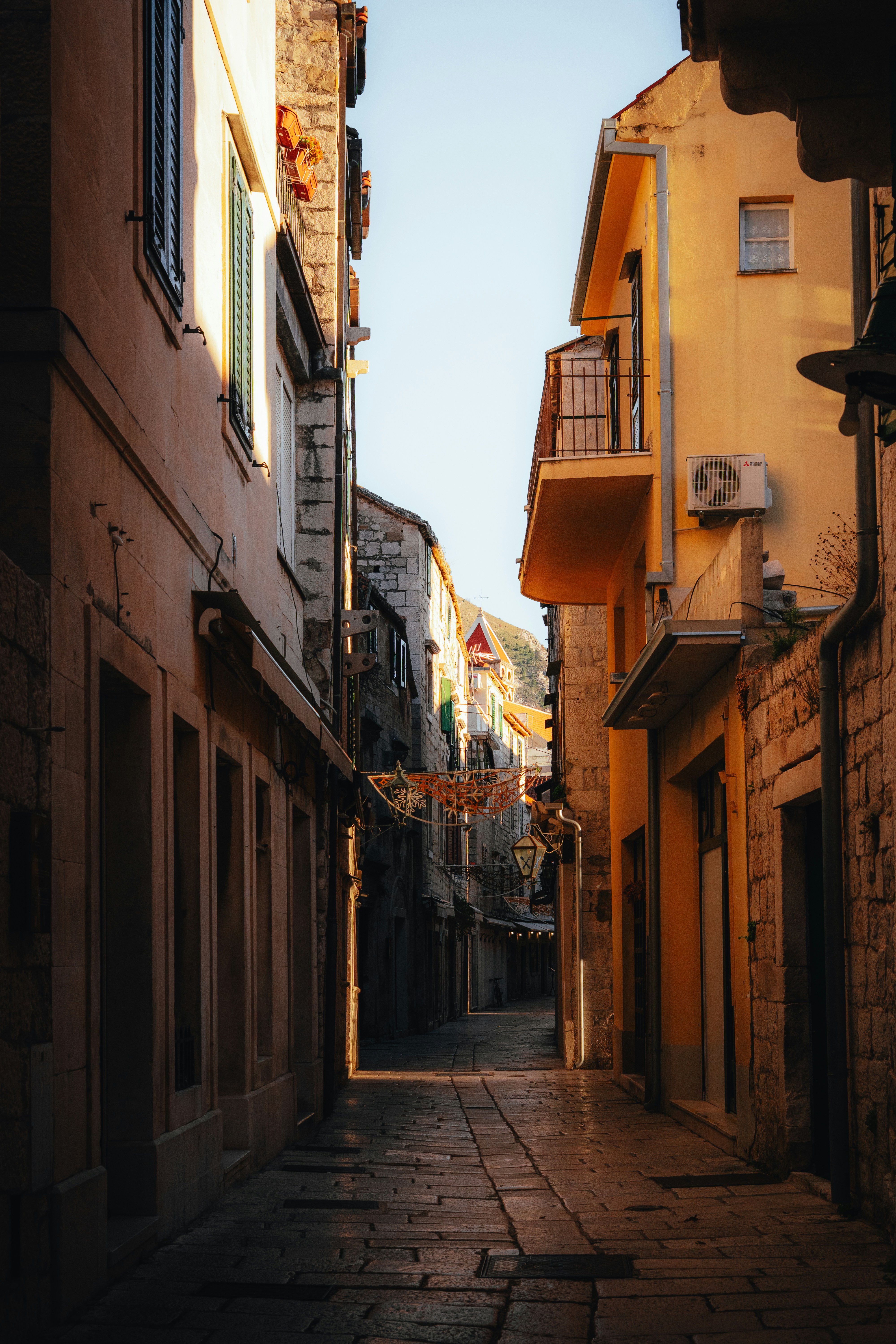Narrow sunlit alley lined with warm-toned buildings and hanging string lights, inviting a calm stroll through the historic street.