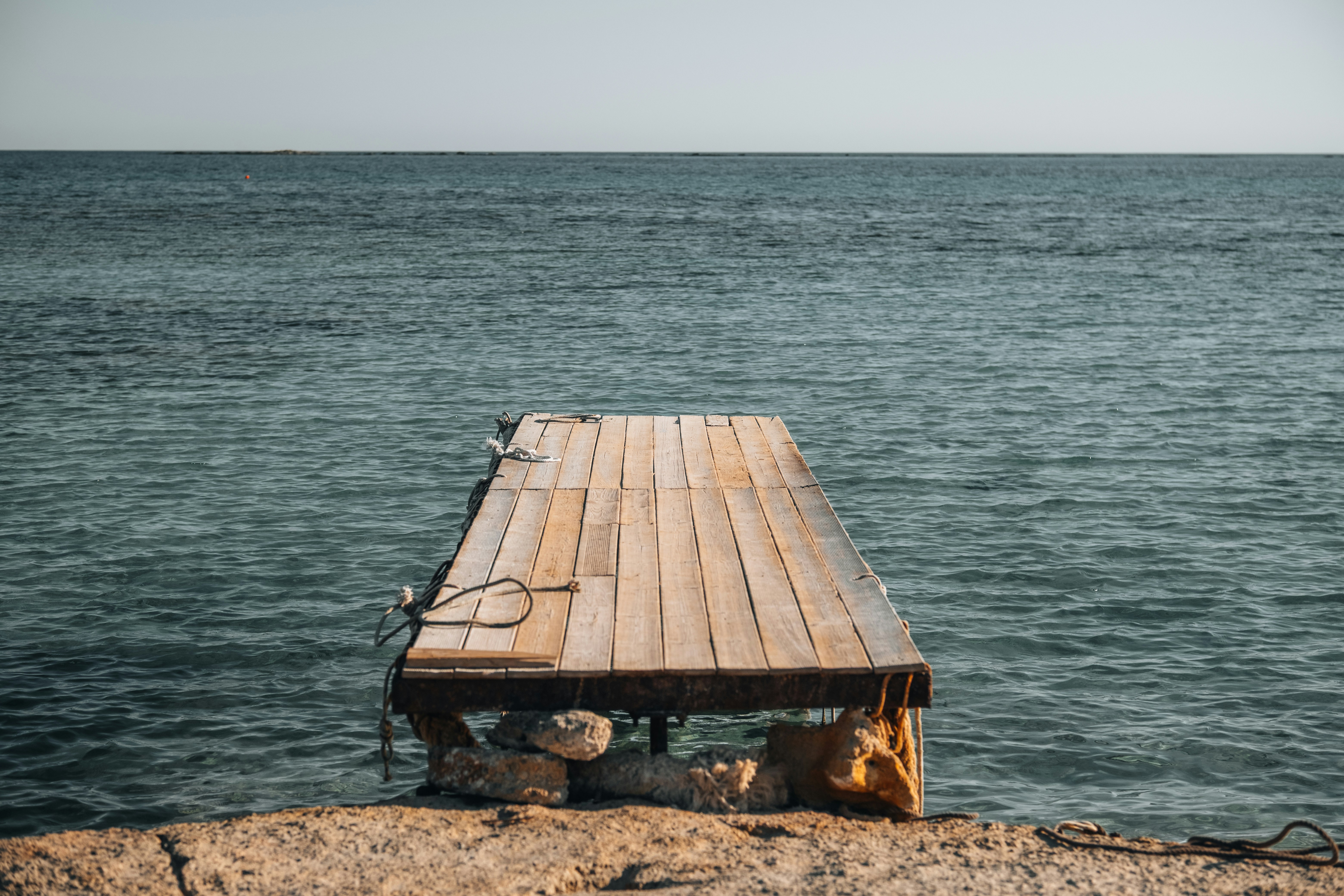 A weathered wooden pier extends toward calm blue water, anchored by boulder supports at the shoreline.