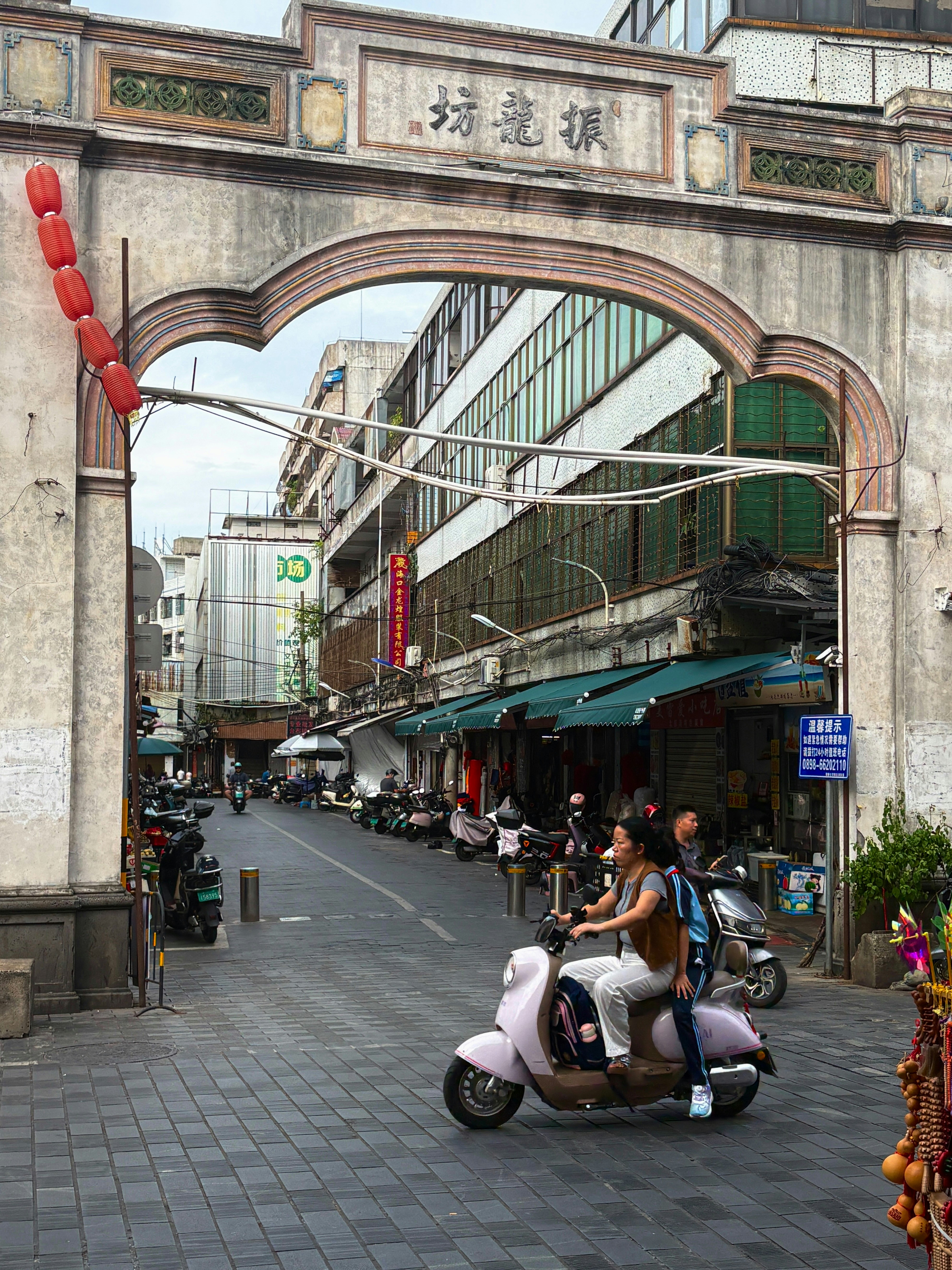 Gateway to a Market Street: Scooters and Lanterns Under the Arch