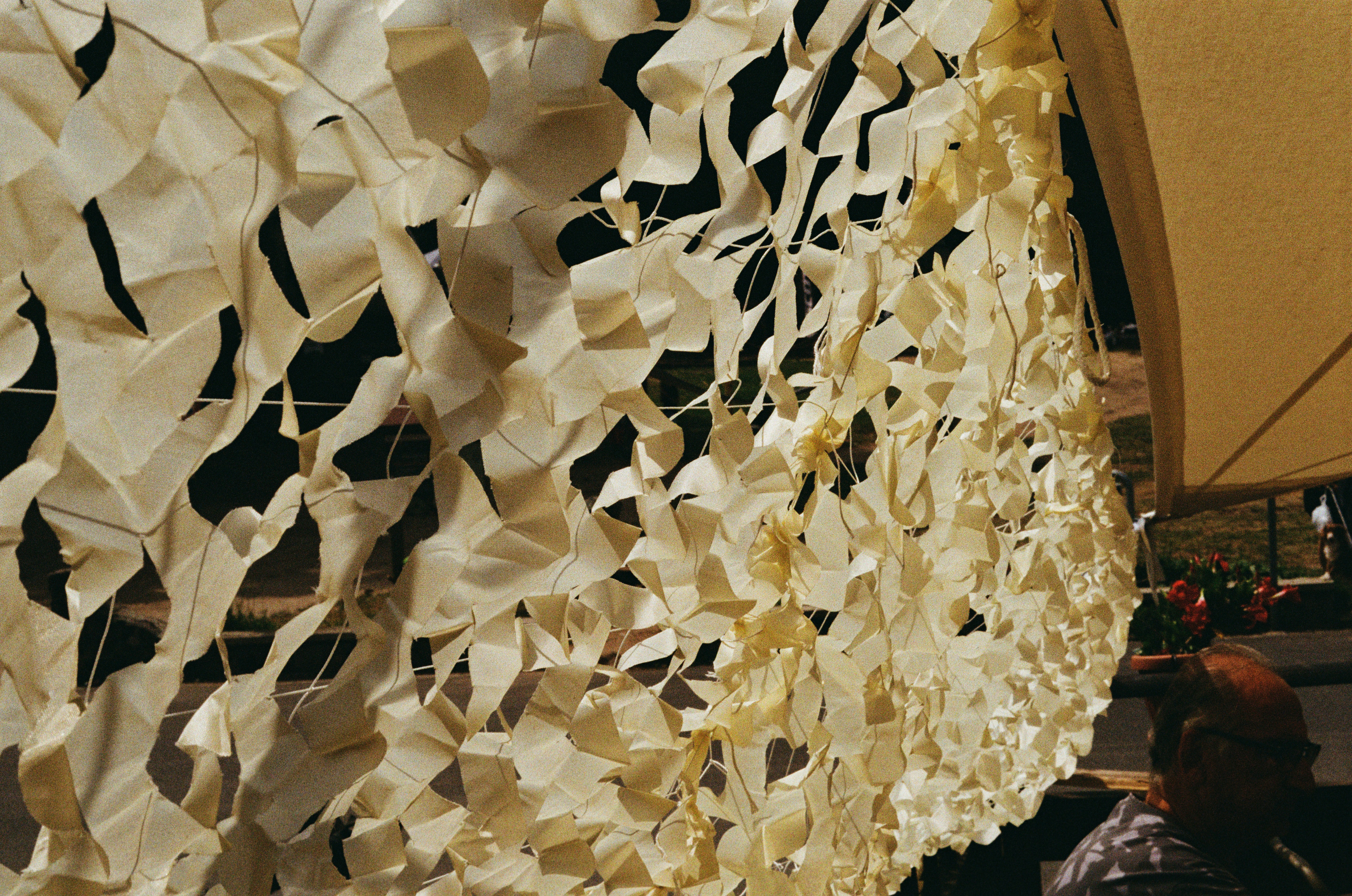Close-up of a cream paper installation with interwoven shapes, partially obscuring a dark background and a hint of crowd. An abstract, textured sculpture dominates the frame.