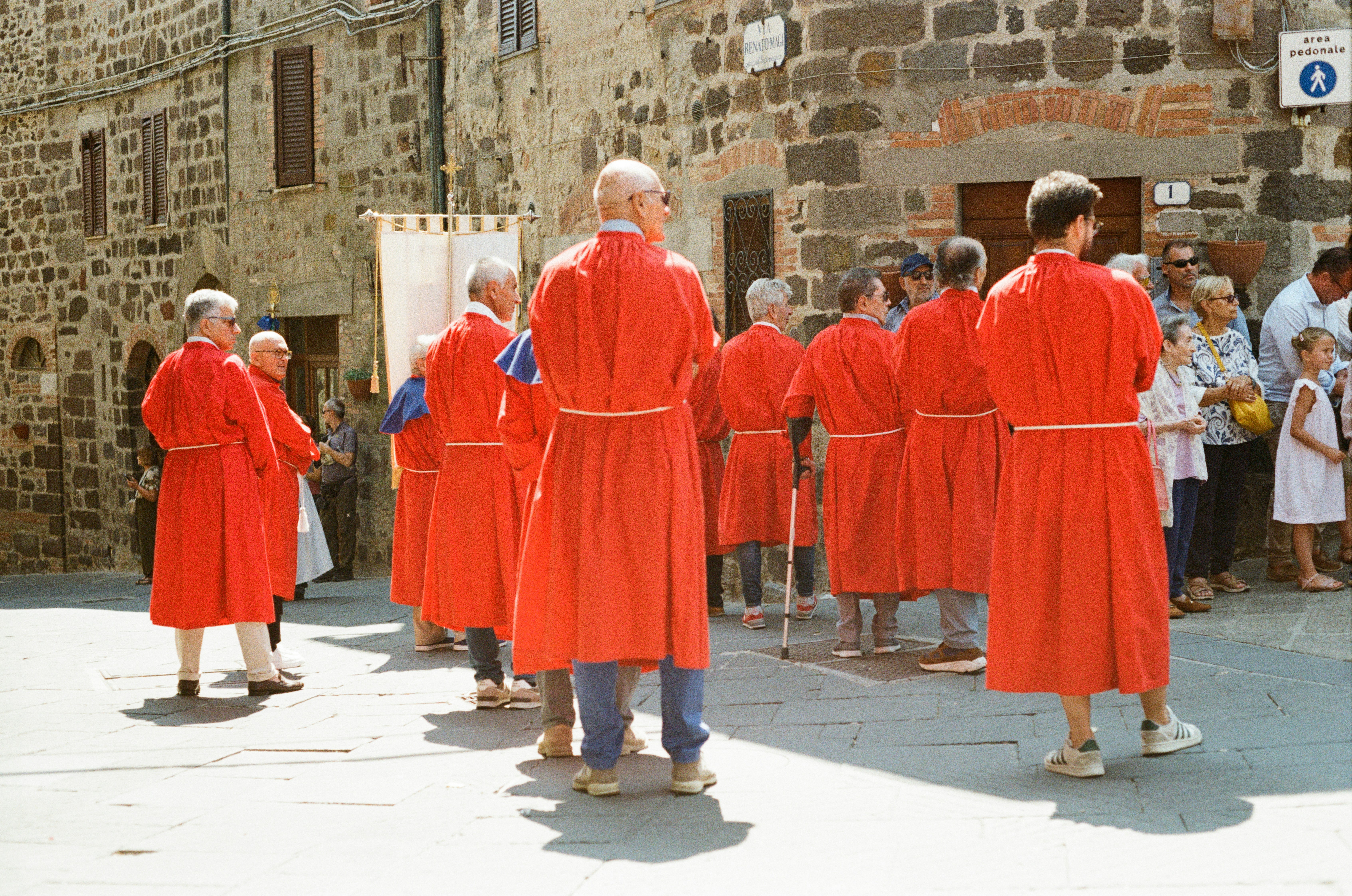 Red-robed procession in a sunlit cobblestone plaza