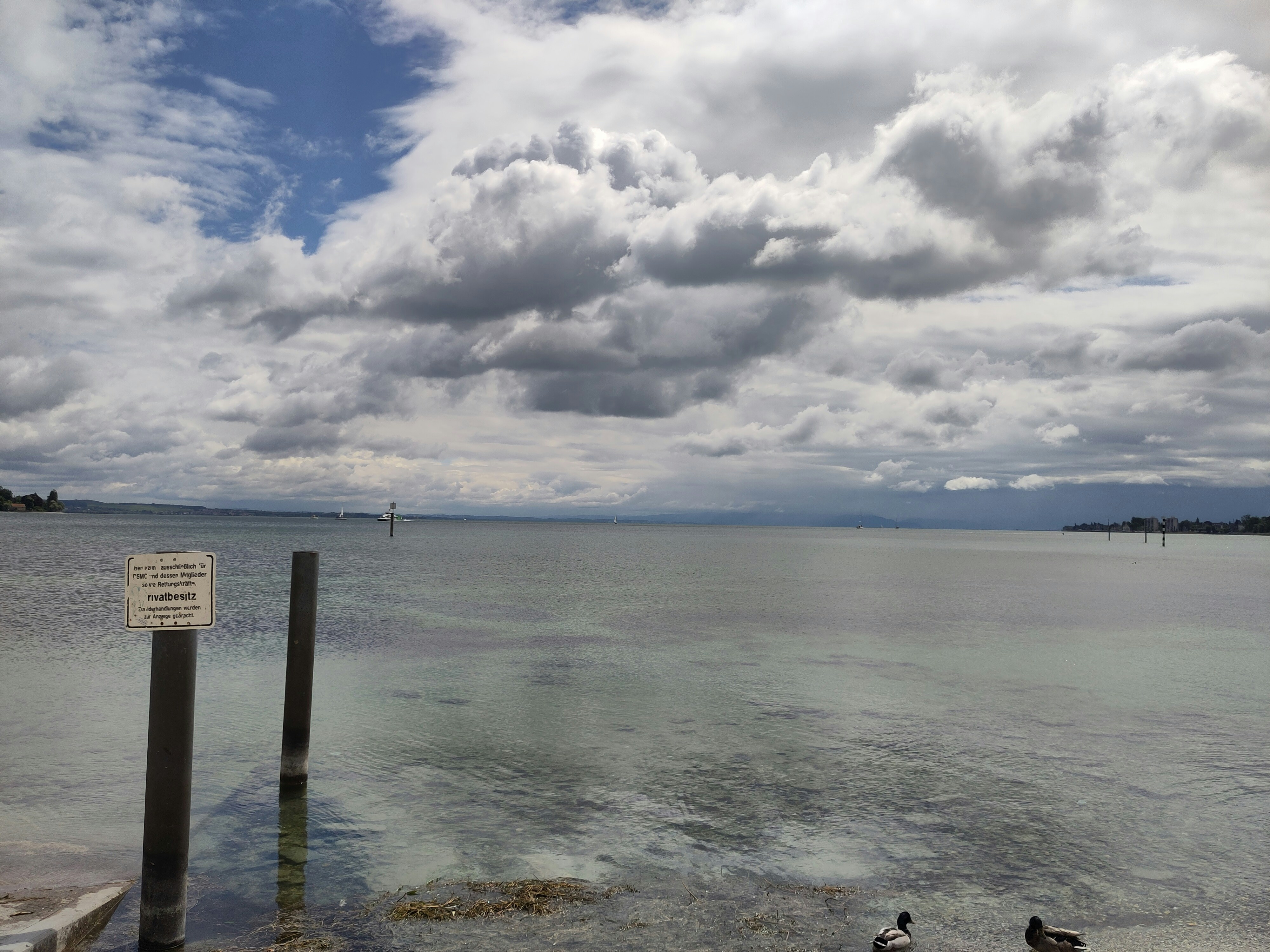 Calm coastal scene with clear shallow water and distant horizon under dramatic clouds; a minimal shoreline conveys peaceful ambience without prominent focal subjects. note: landscape capture.