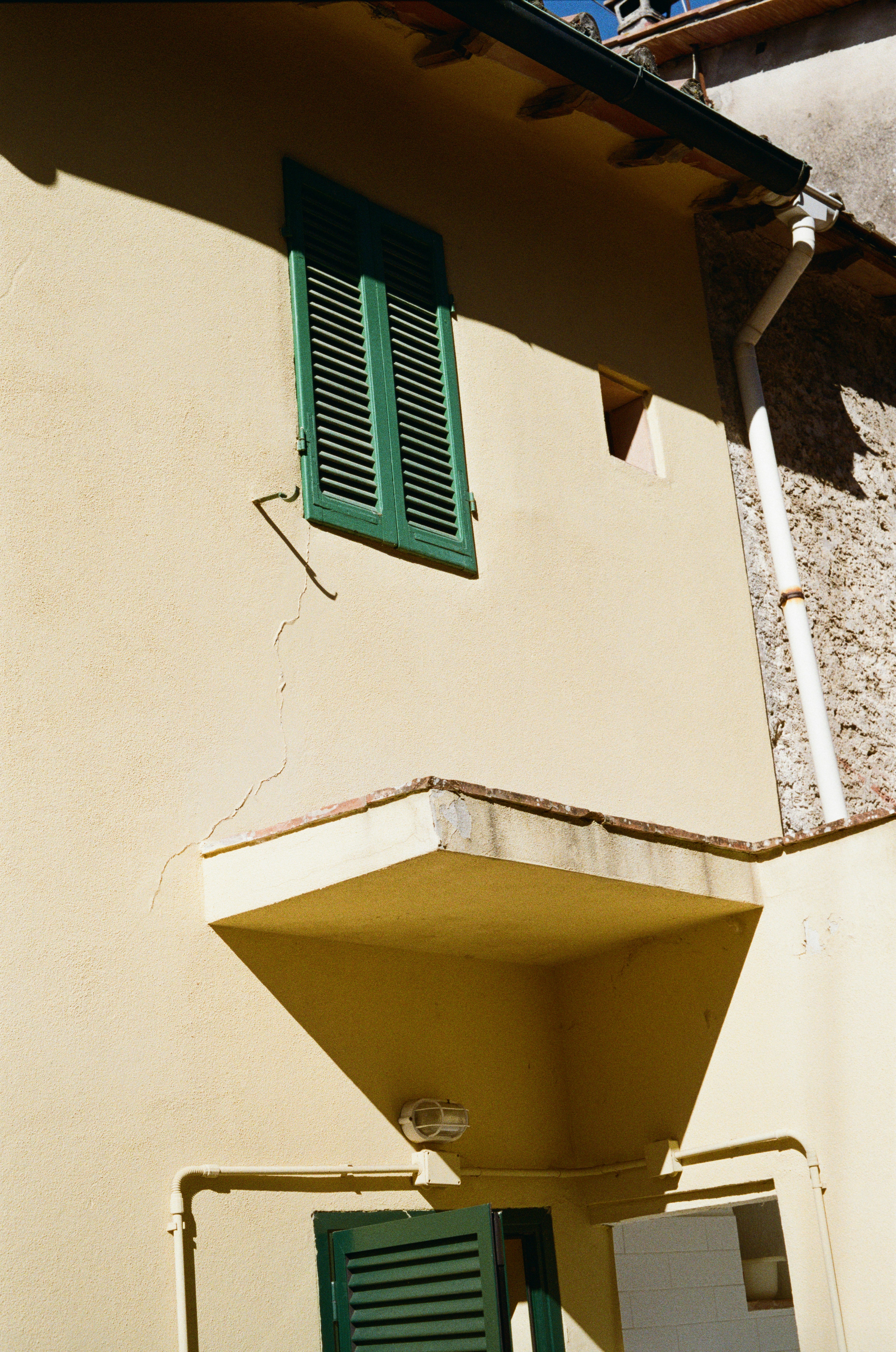 Sunlit Beige Facade with Green Shutter under Coping Angle