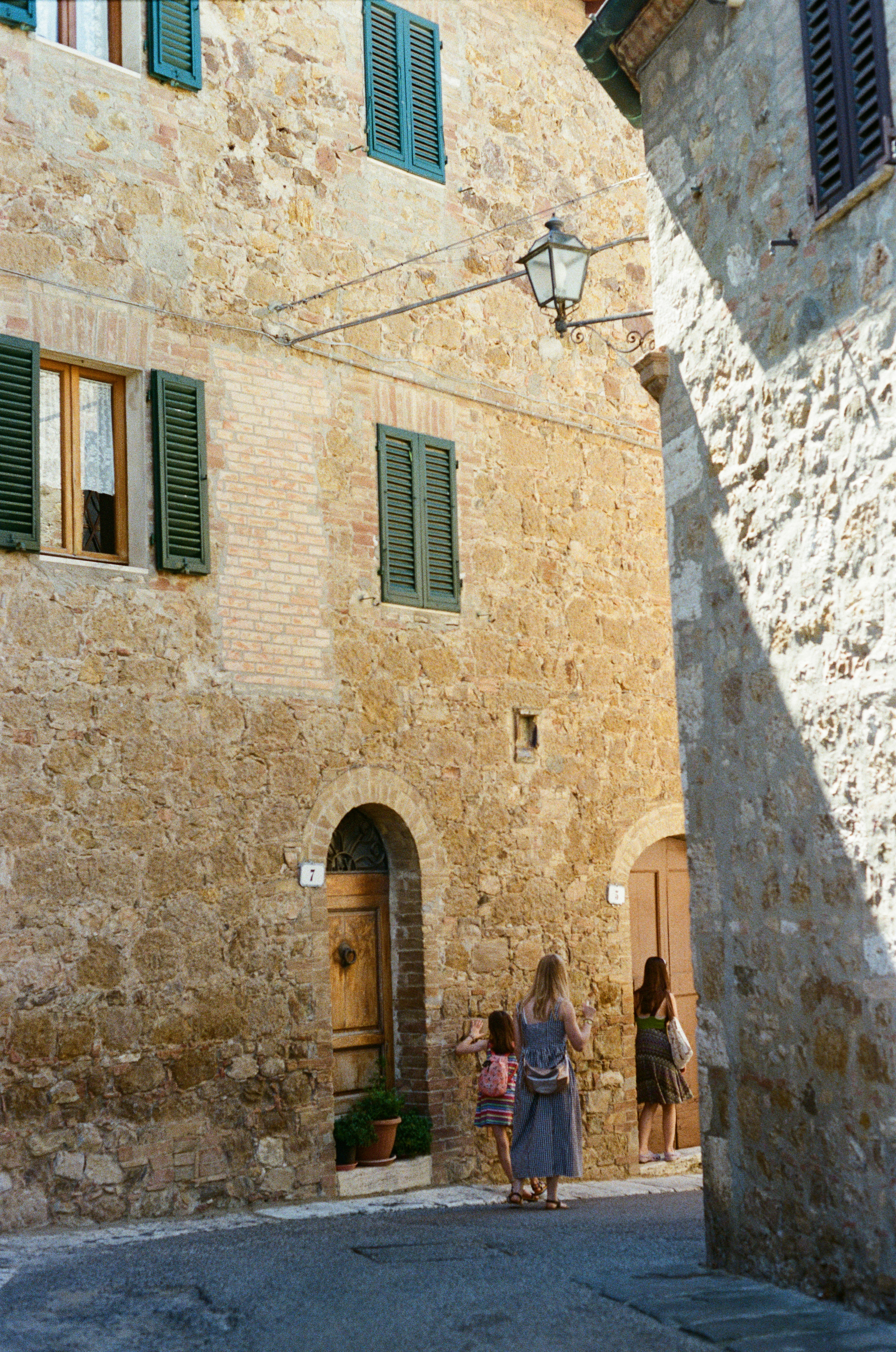 Sunlit stone street: two women and a child pause by arched doors