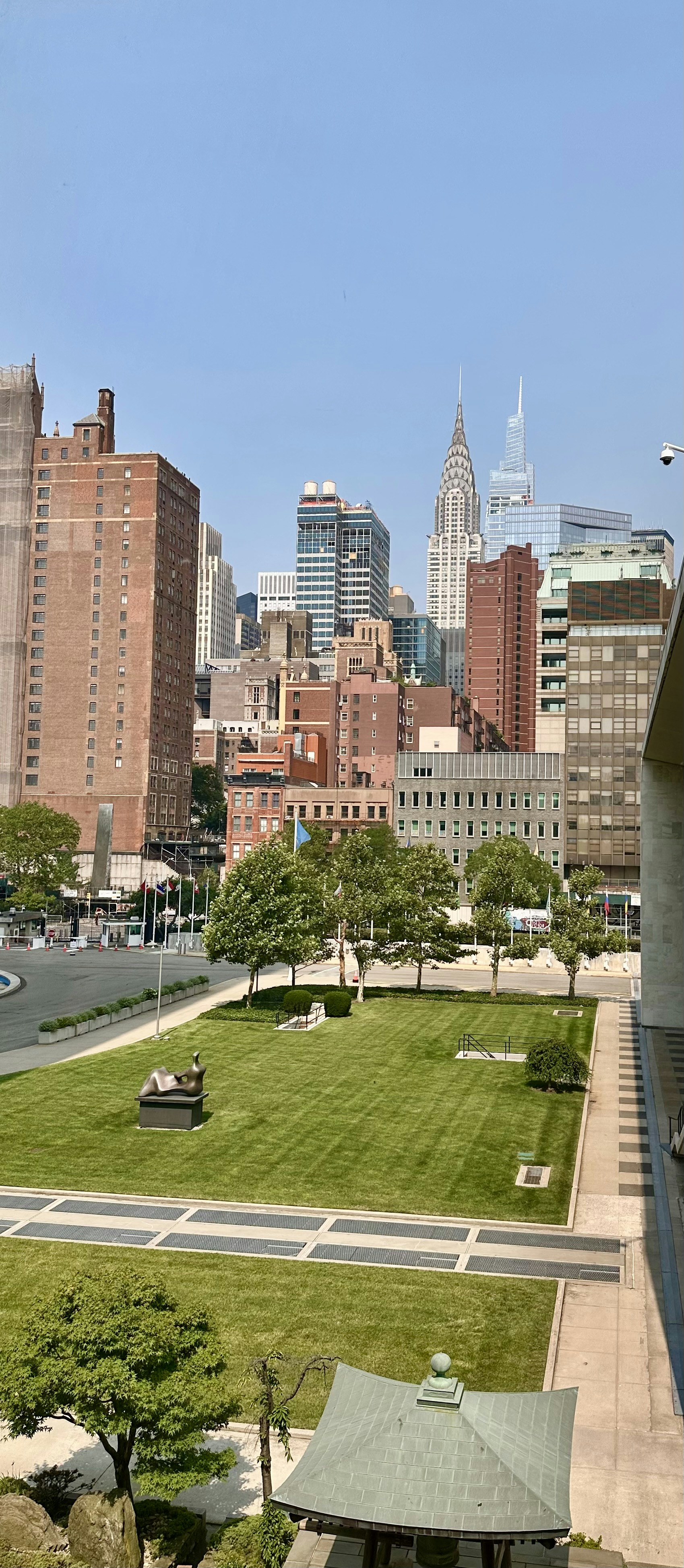 Sunlit cityscape with a manicured park in the foreground and tall skyscrapers in the background, captured from a high vantage point. This scene emphasizes the contrast between green space and urban architecture.
