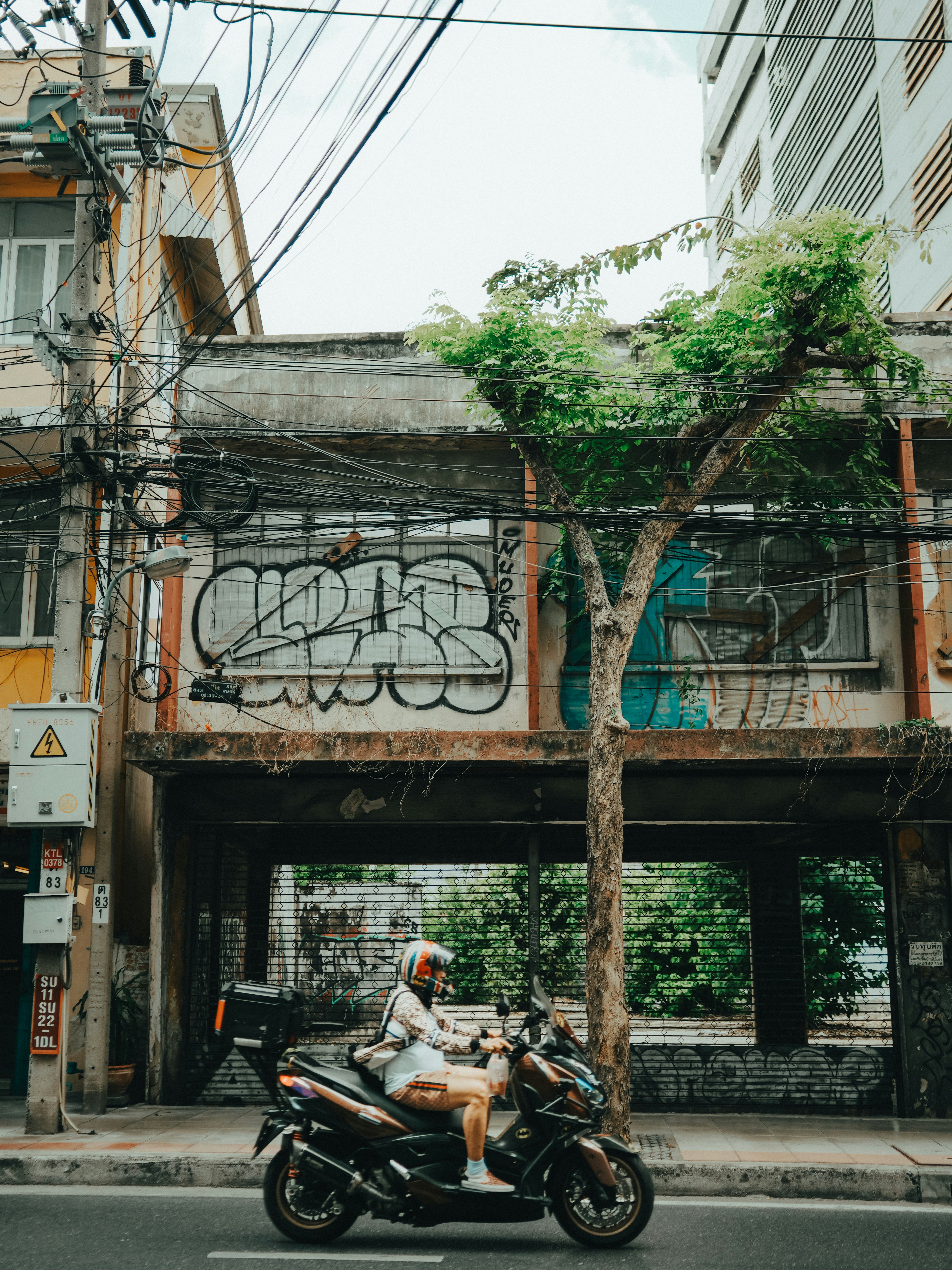 Motorcycle Taxi Crossing the Graffiti-etched Urban Corridor