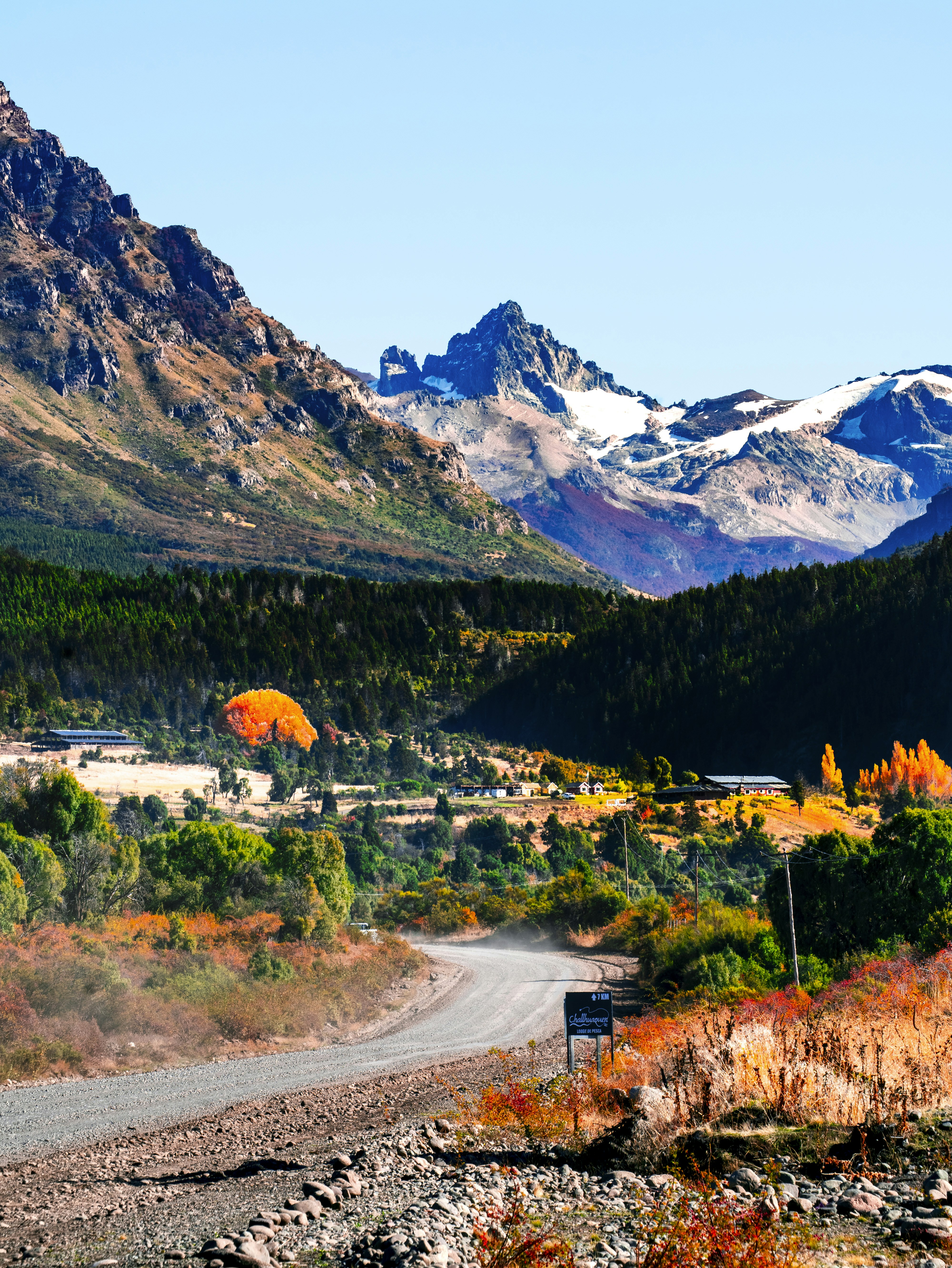 Winding dirt road through autumn mountains with snow-capped peaks.