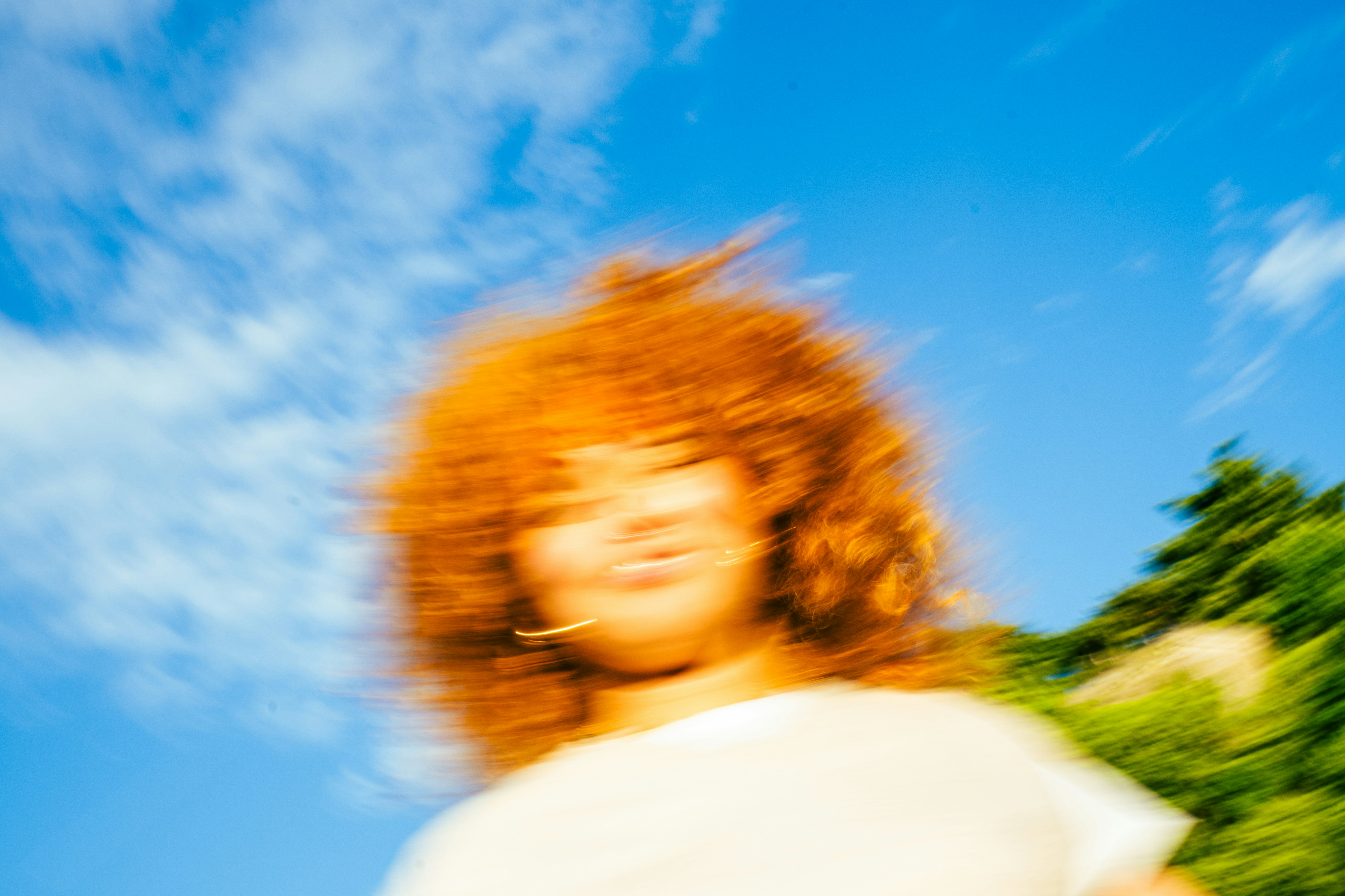 Blurred Portrait in Bright Sky: A Flurry of Orange Hair and Sky-blue backdrop