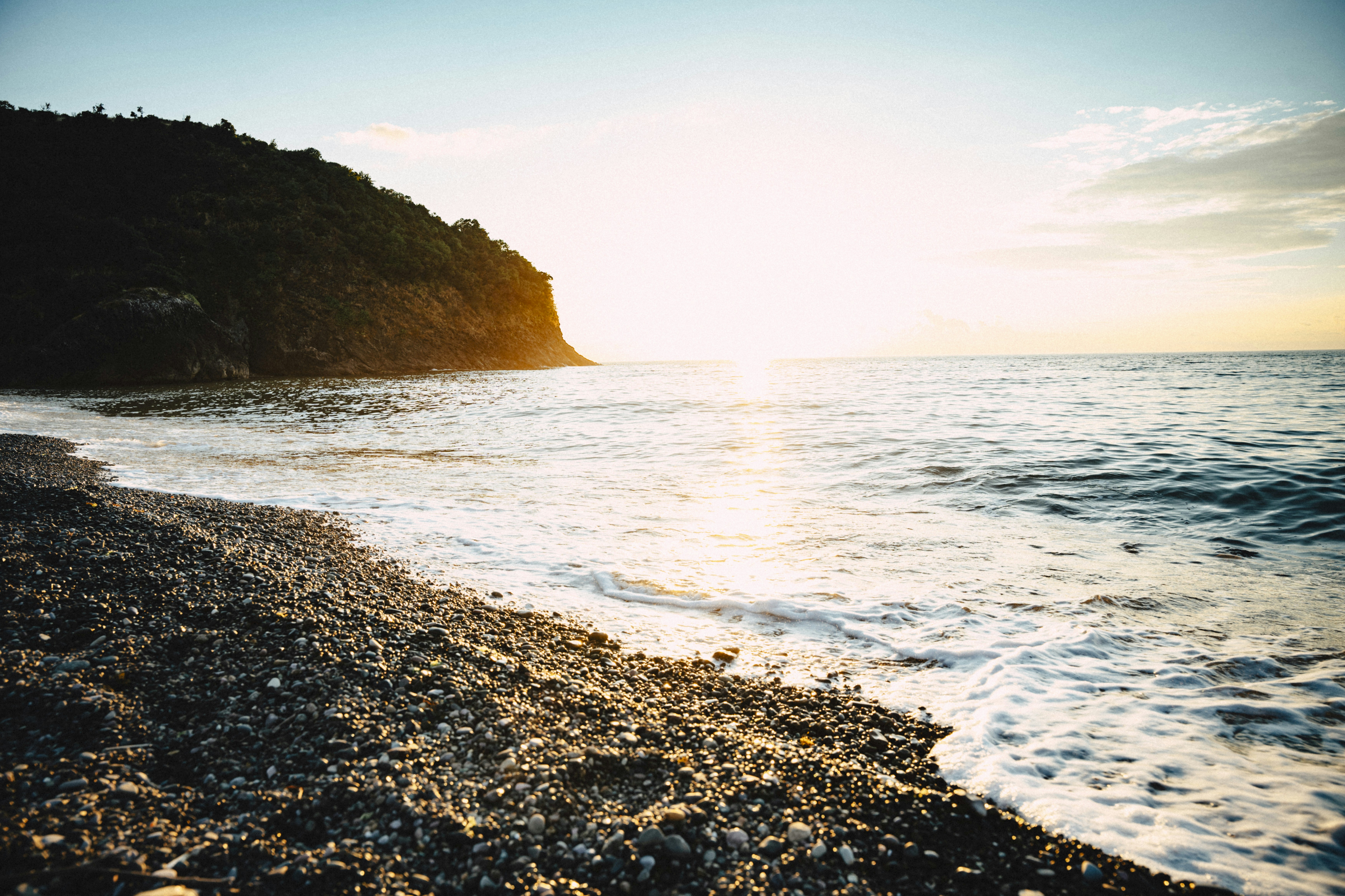 Sunlit shoreline where sea meets rugged headland at golden hour