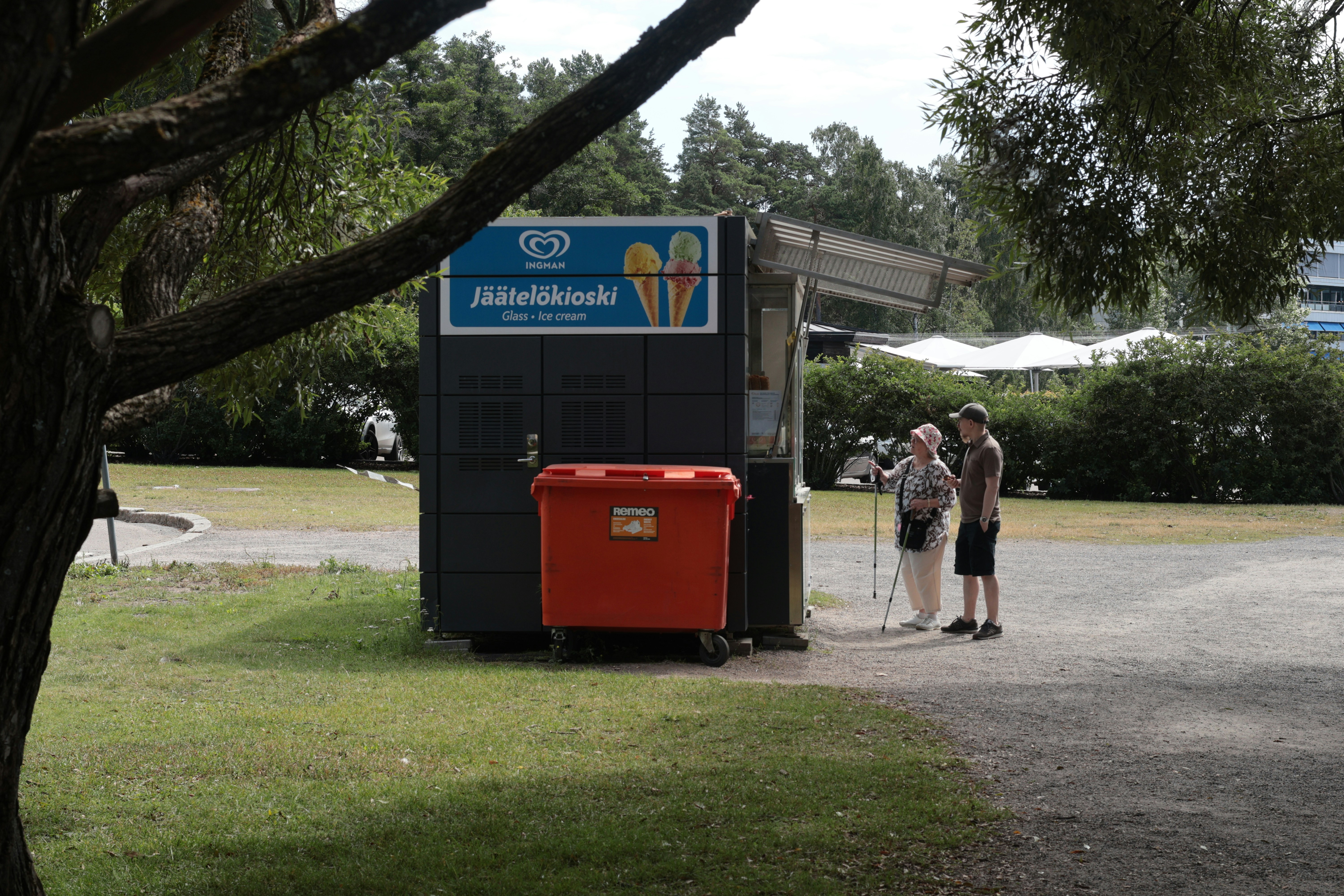 Red Waste Bin and two people under a shelter in a park backdrop