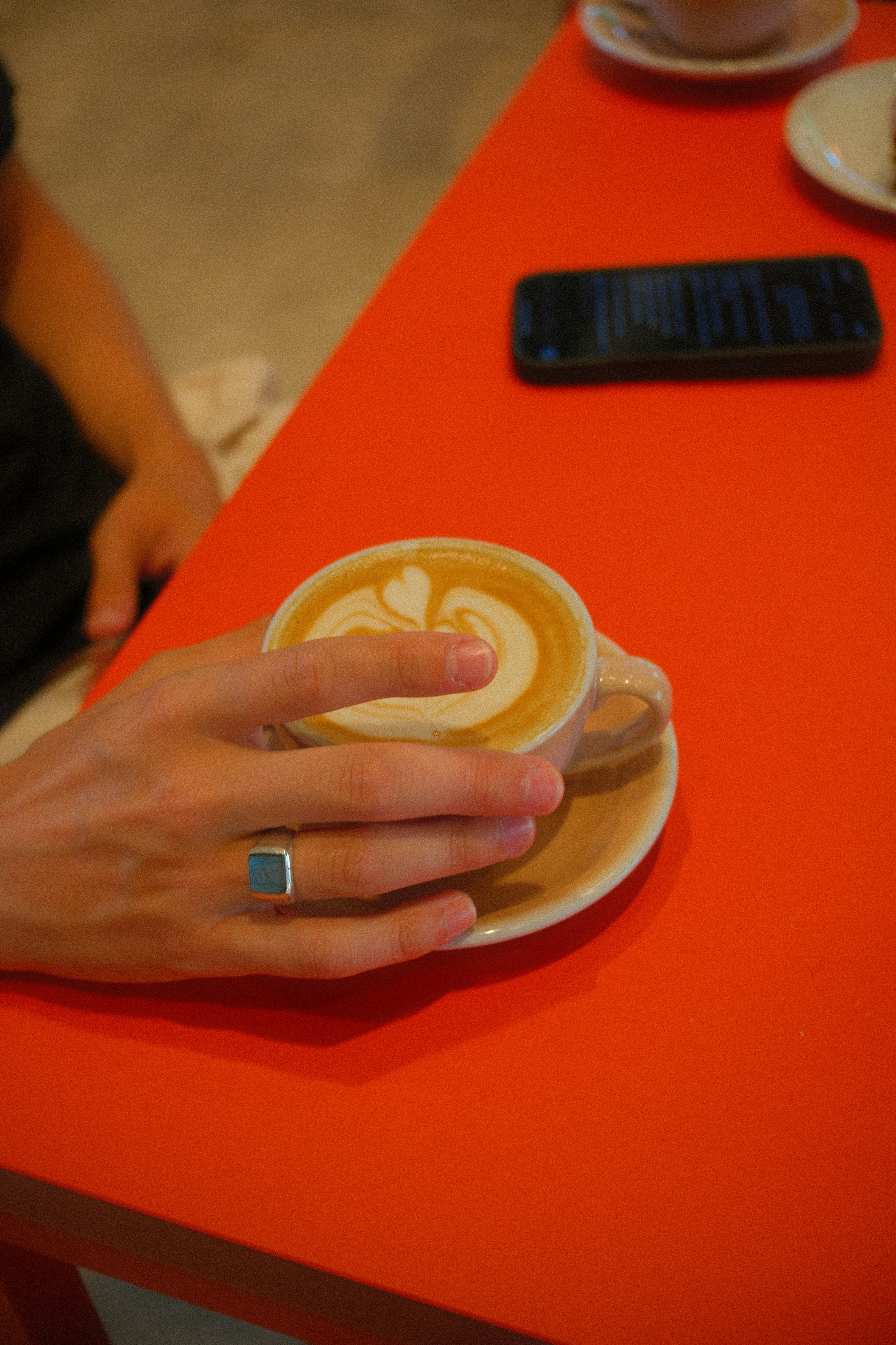 Hand holding latte art coffee cup on an orange table.