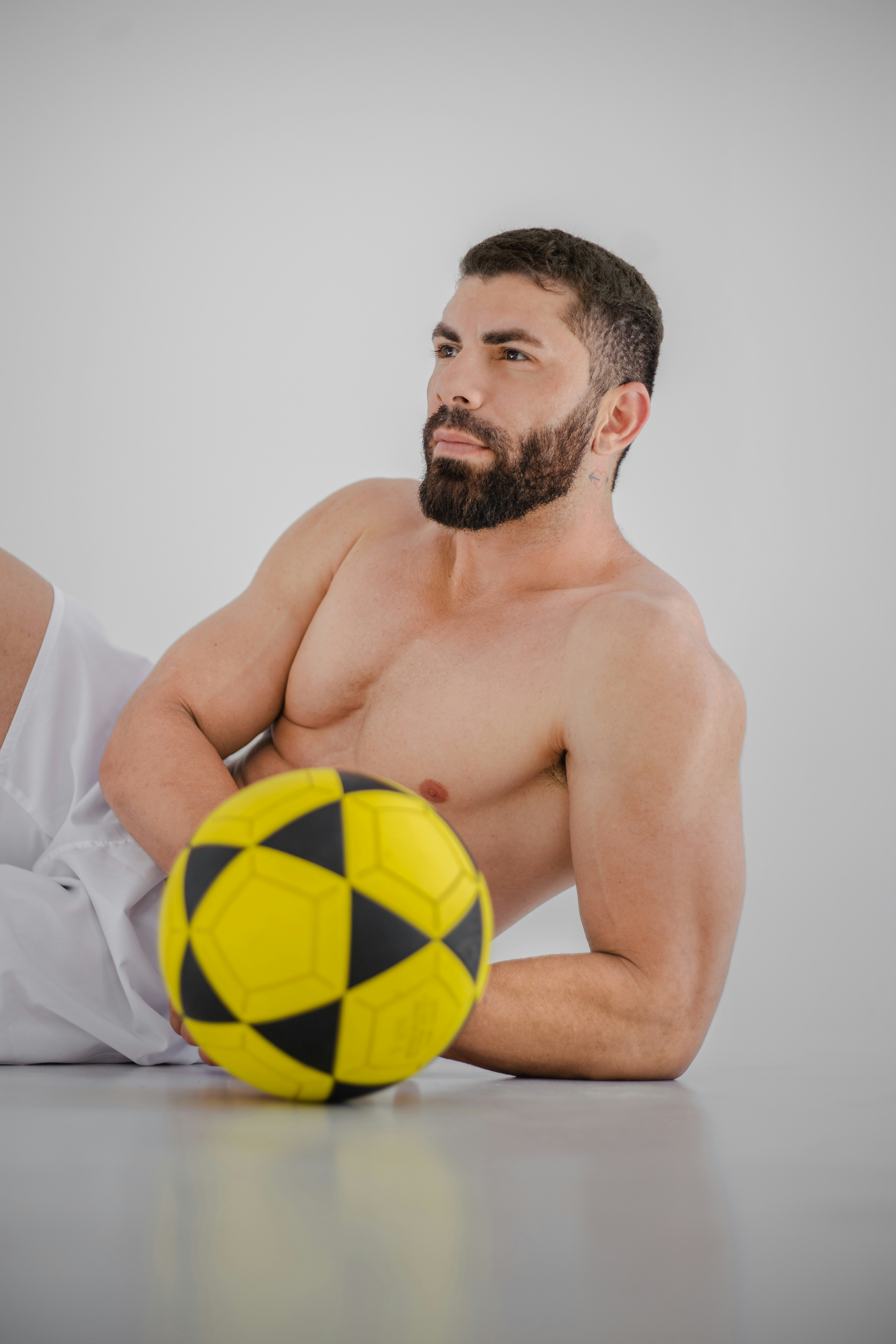 Relaxed athlete with yellow soccer ball in a minimalist studio