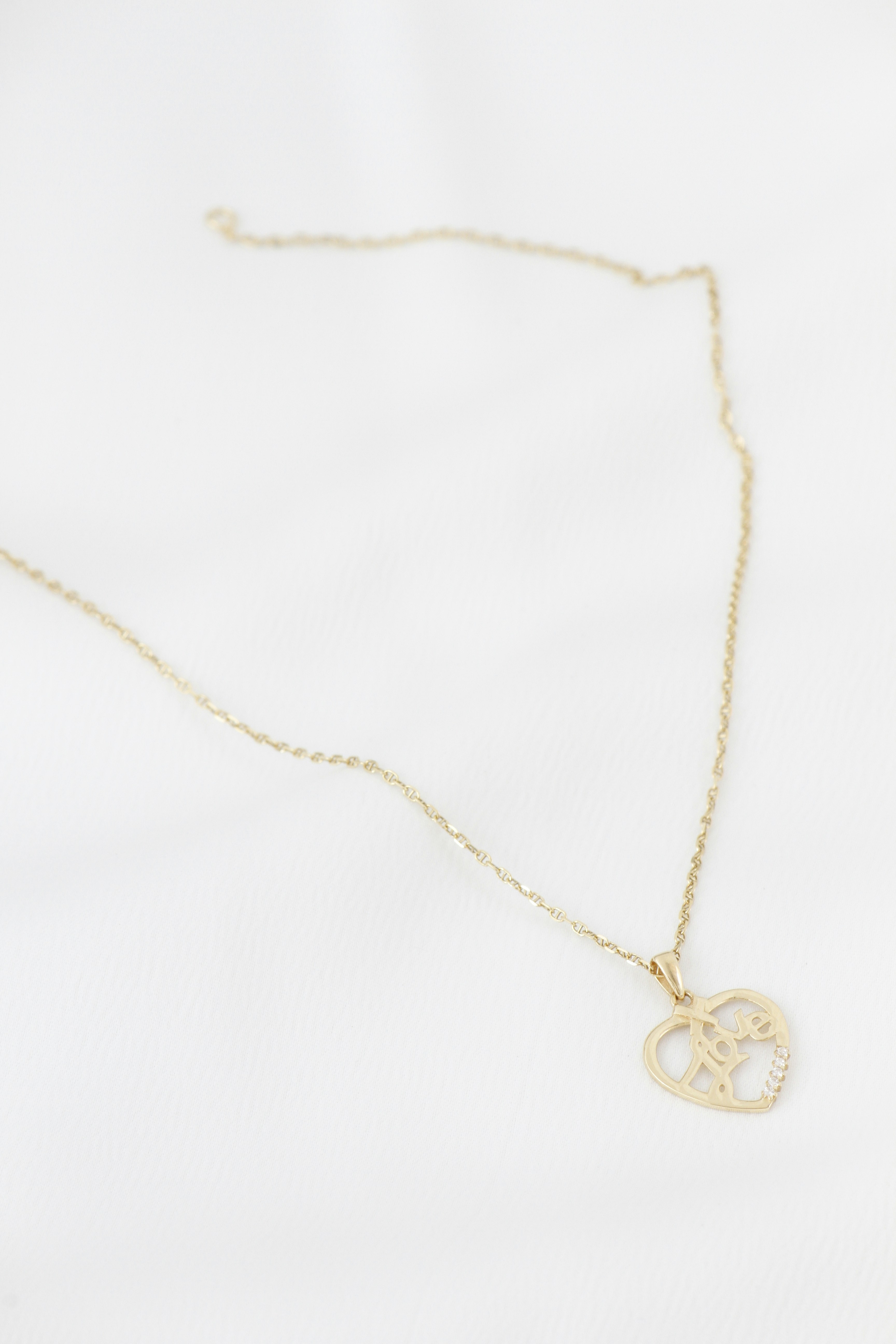 Gold Heart Pendant on Delicate Chain Resting on White Fabric