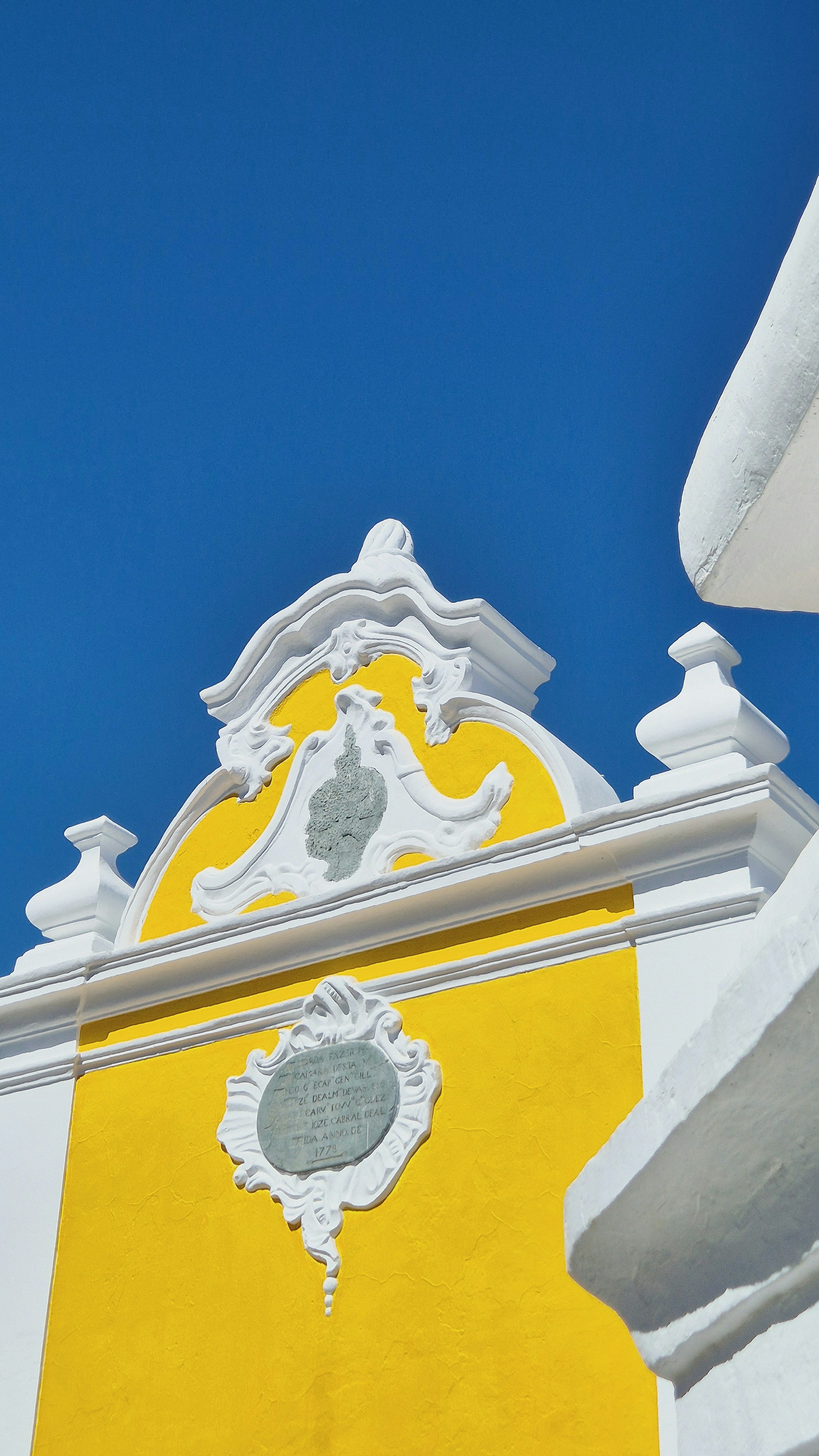 Sunlit yellow façade crowned with white ornamental detailing under a cobalt sky