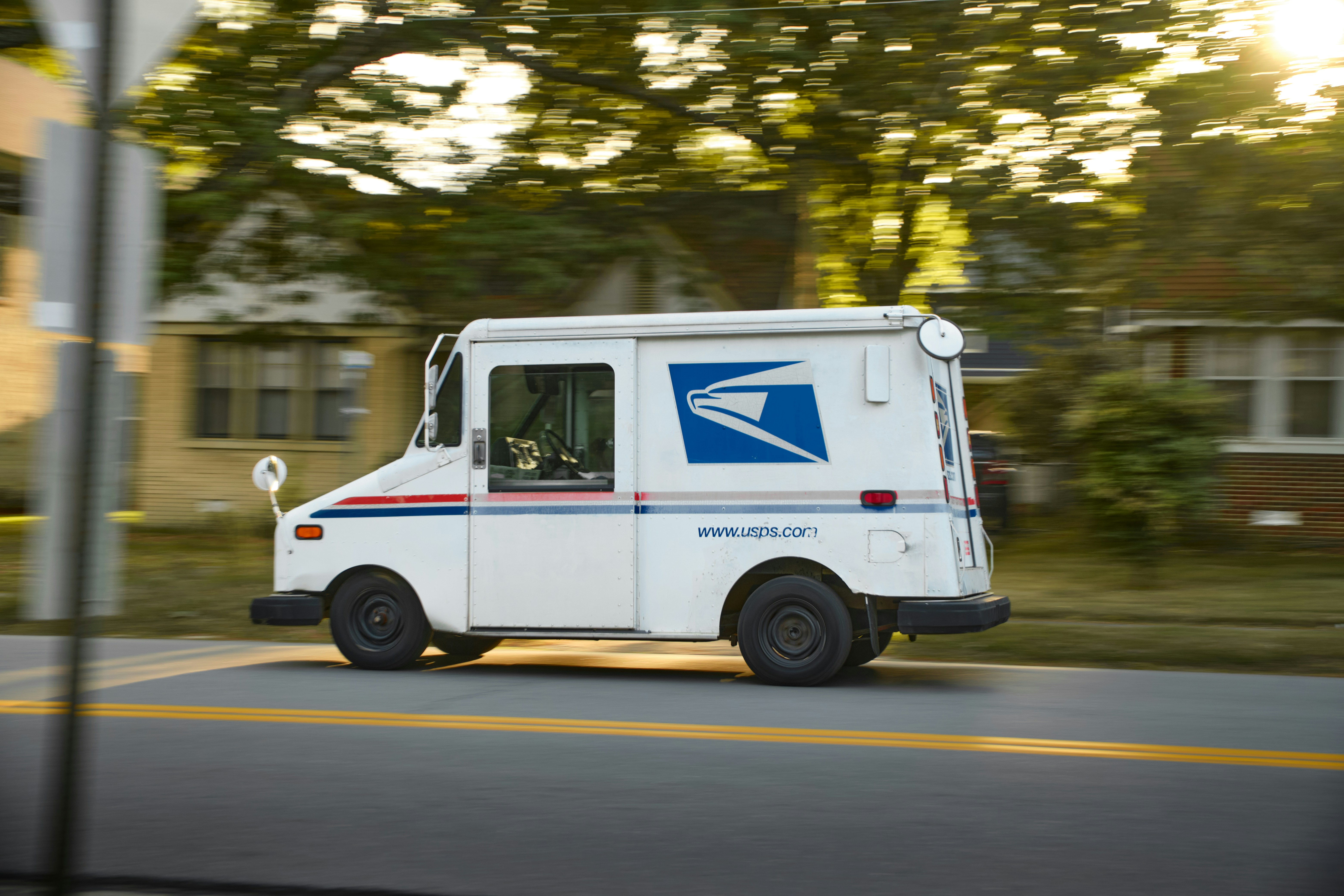Motion in Transit: A USPS Parcel Van Drives Past a Suburban Row