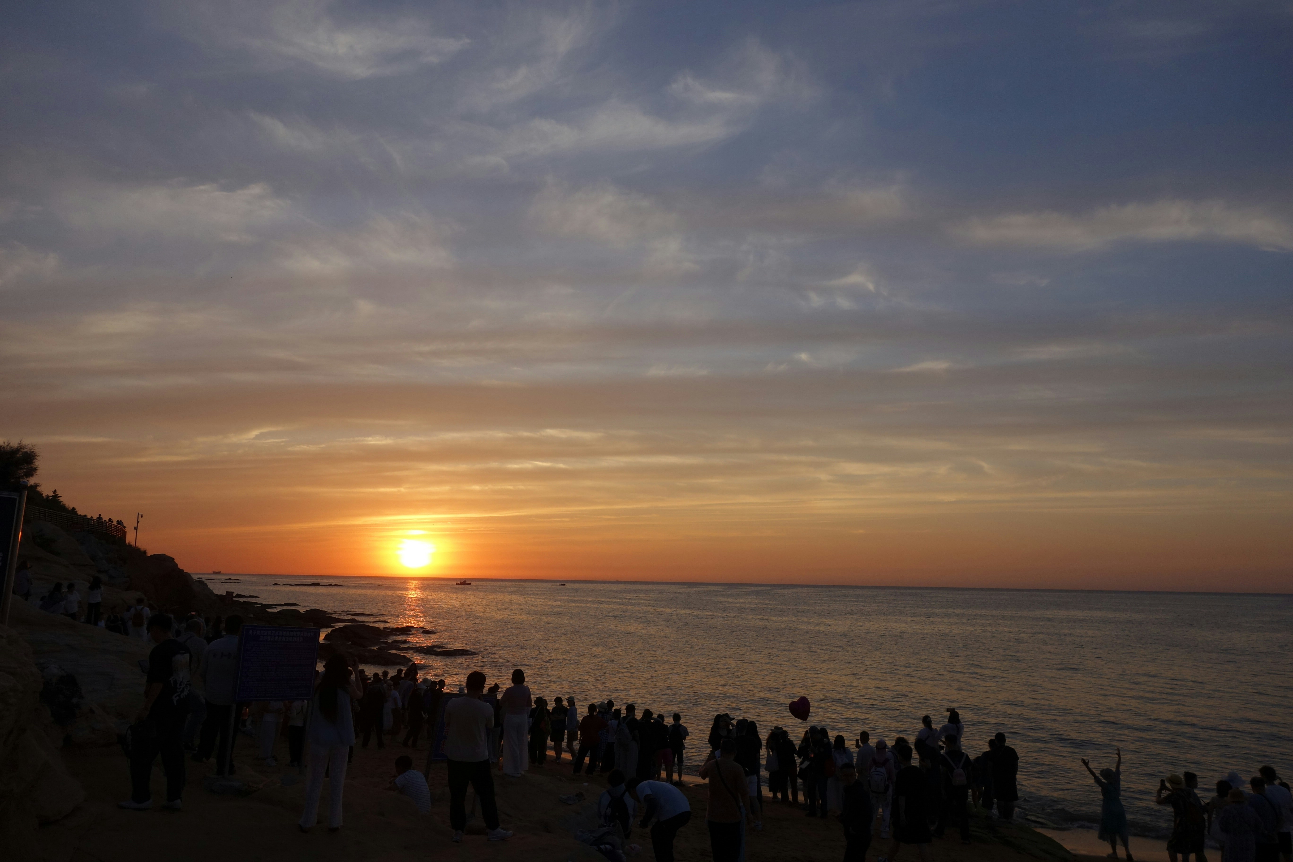 Crowd watches a vibrant sunset over the sea.