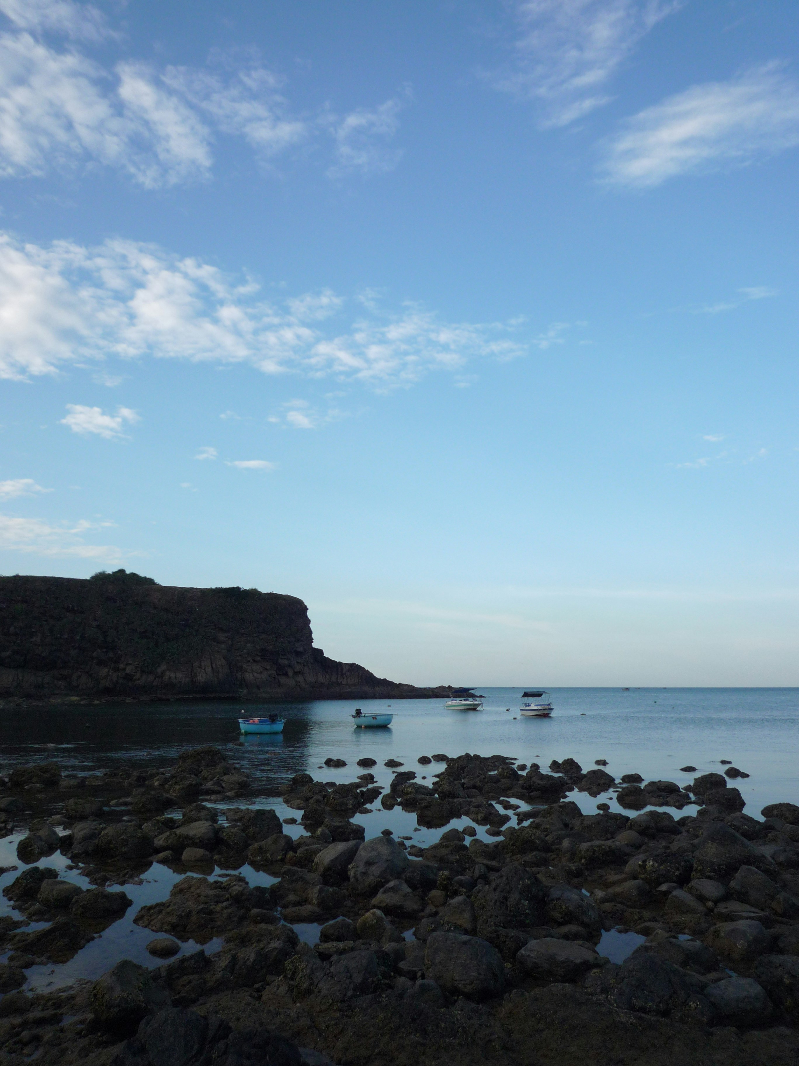 Coastal Silhouette: Boats Anchored at Dusk by a Rocky Shore