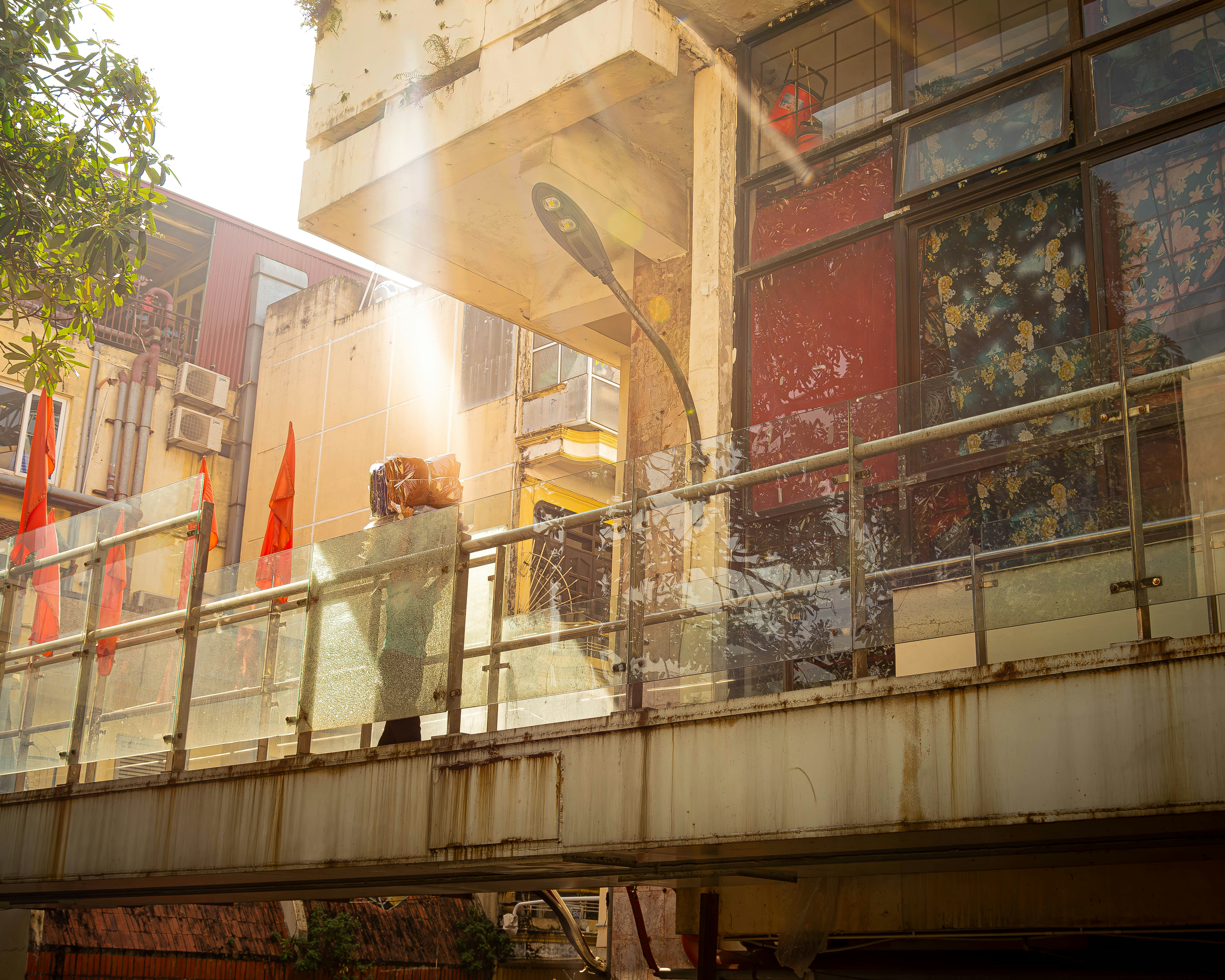 Sunlit Balcony Walk: A pedestrian silhouette through a glass-encased bridge