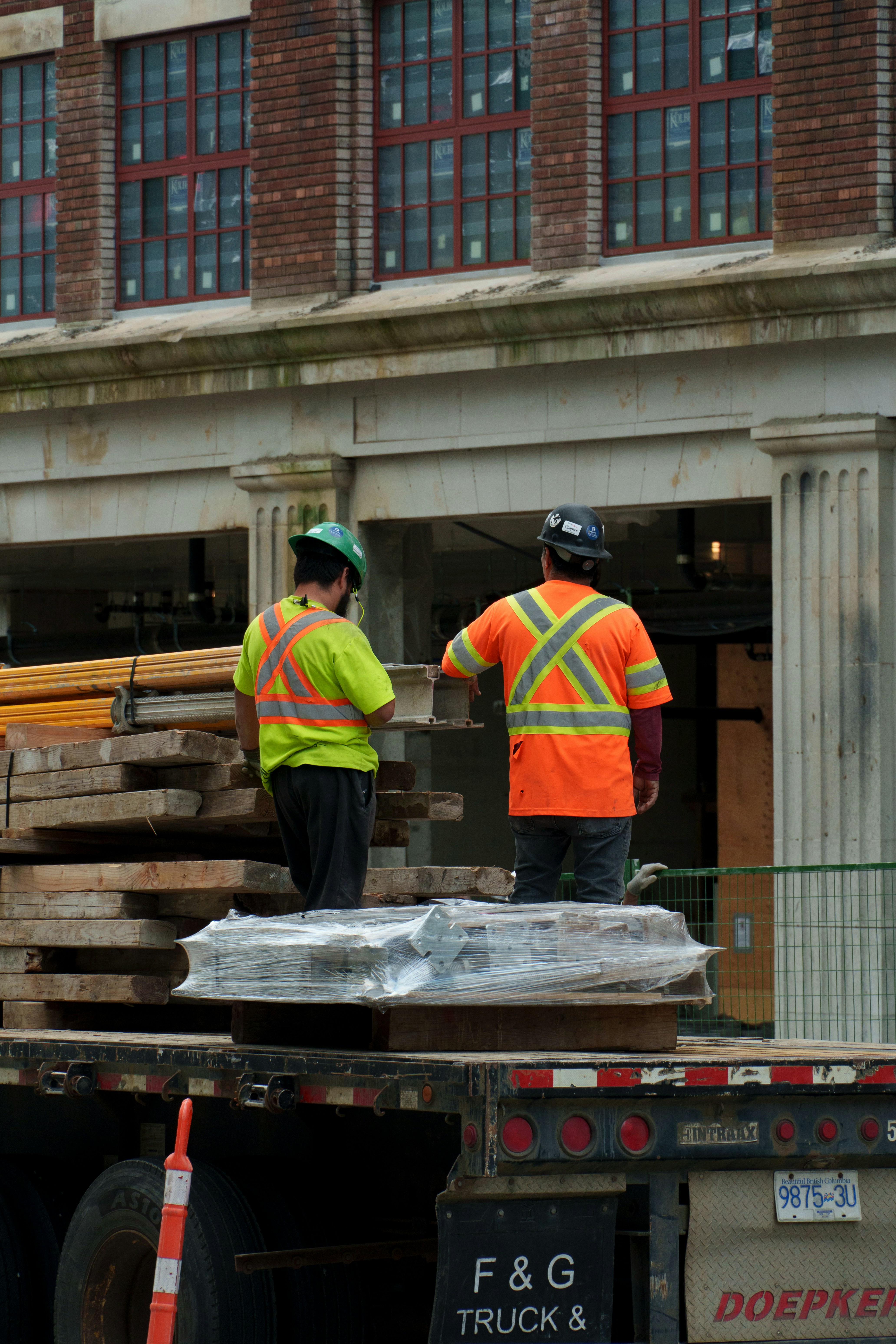 Crew in Neon Safety Vests Inspect a Loaded Flatbed at a Historic Brick Building