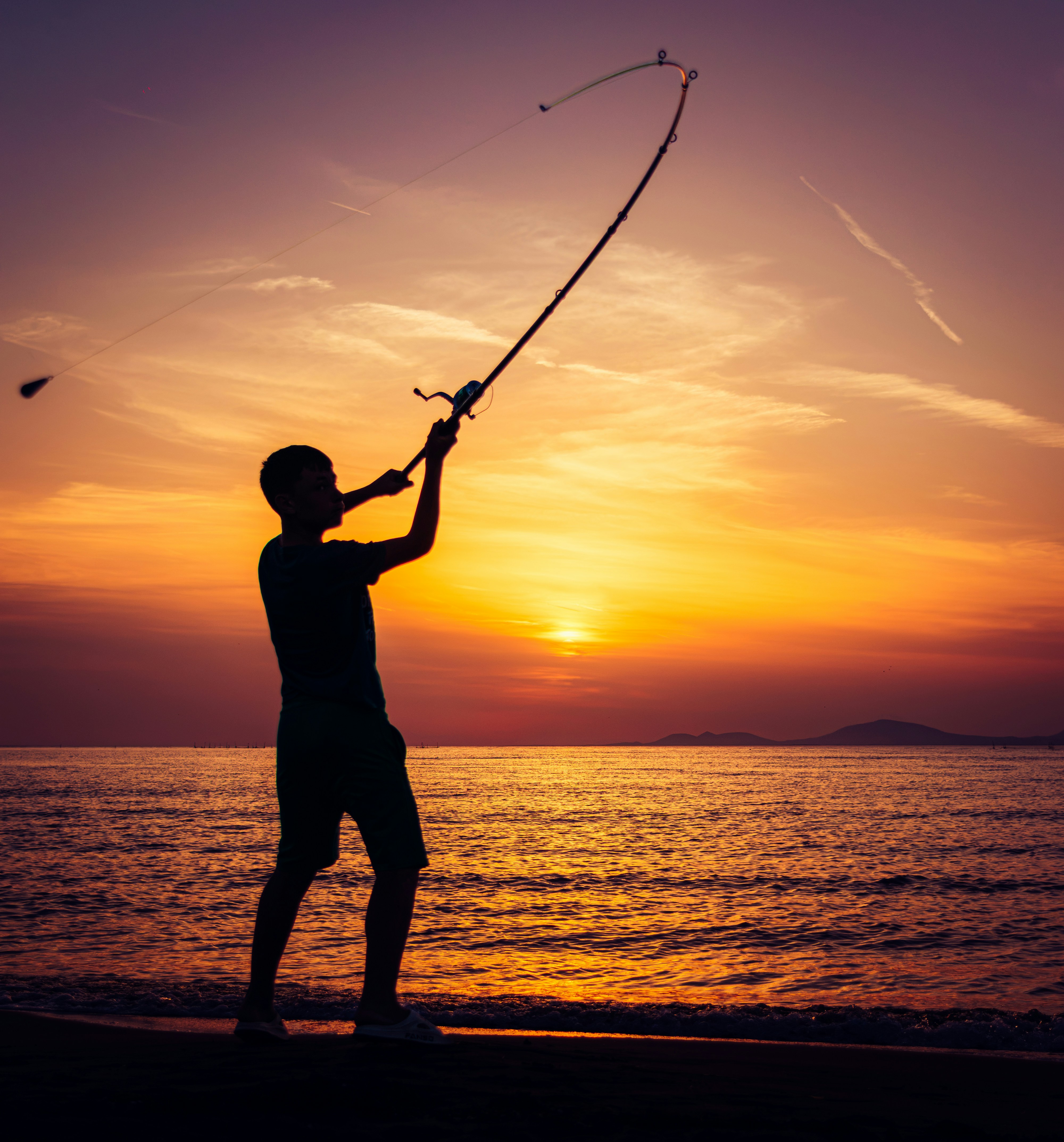 Silhouette of a surfer casting a leash toward the sunset
