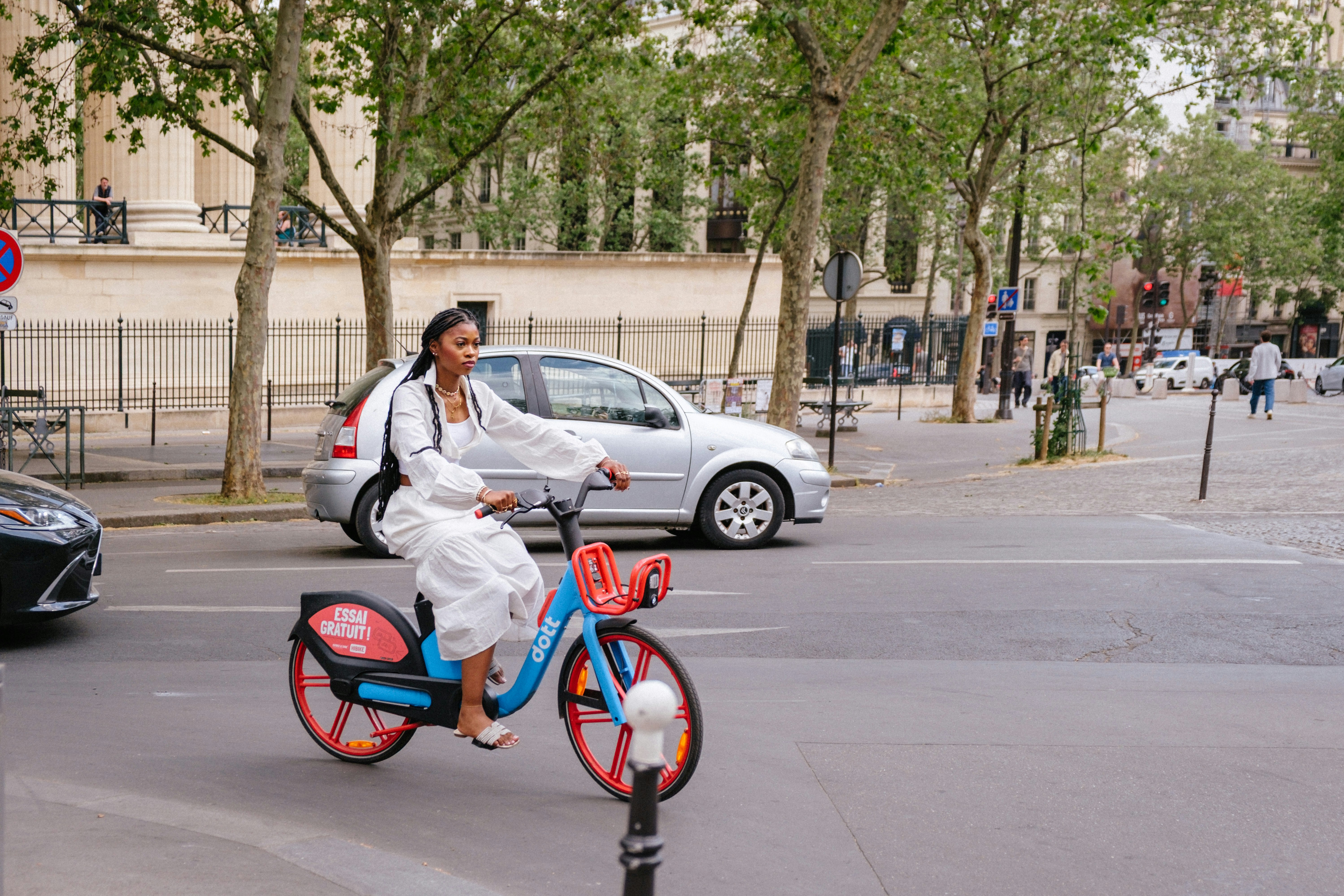 Cyclist in a White Ensemble Rides Through a Parisian Street