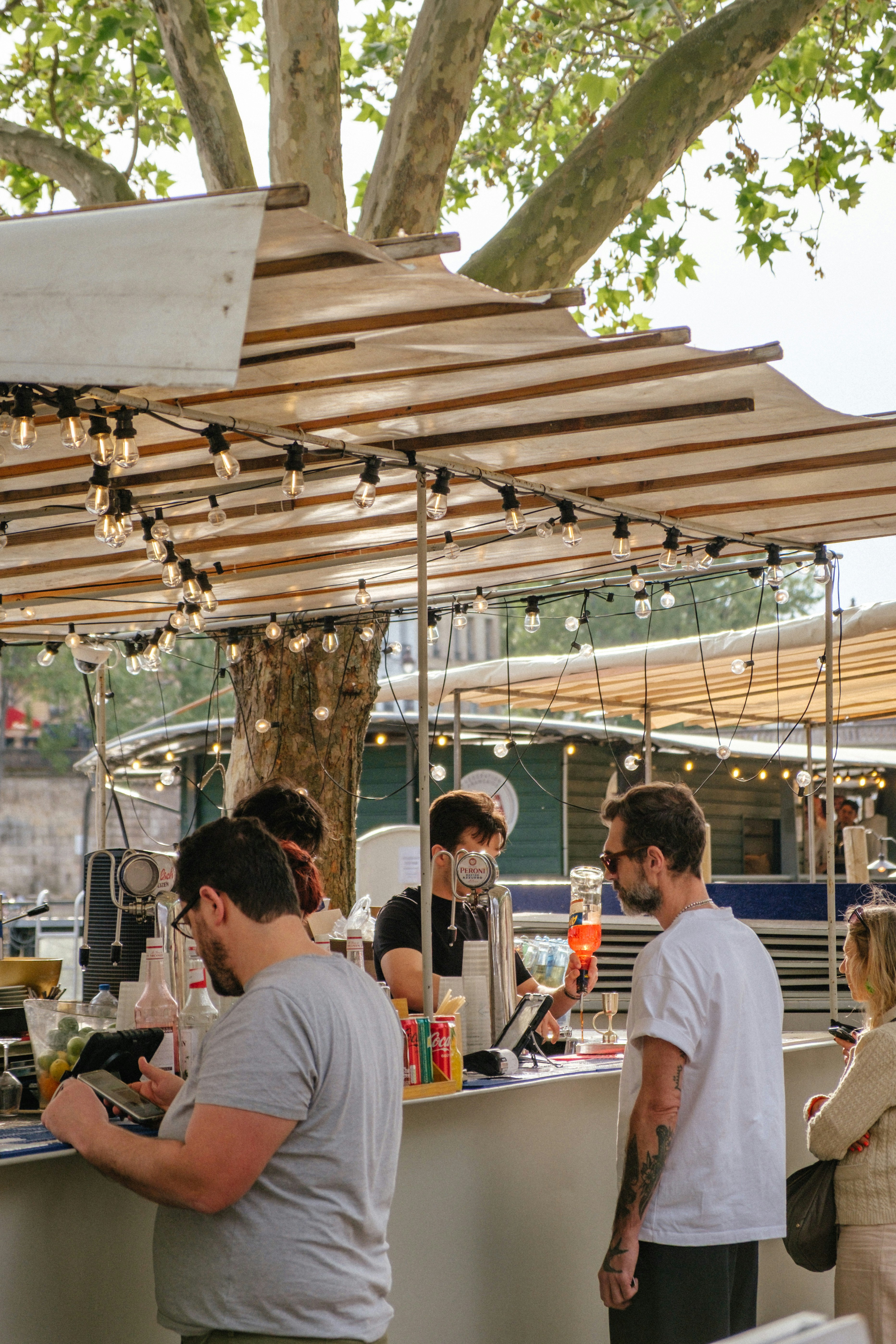Sunlit Outdoor Market Bar: Faces, Drinks, and Strings of Light
