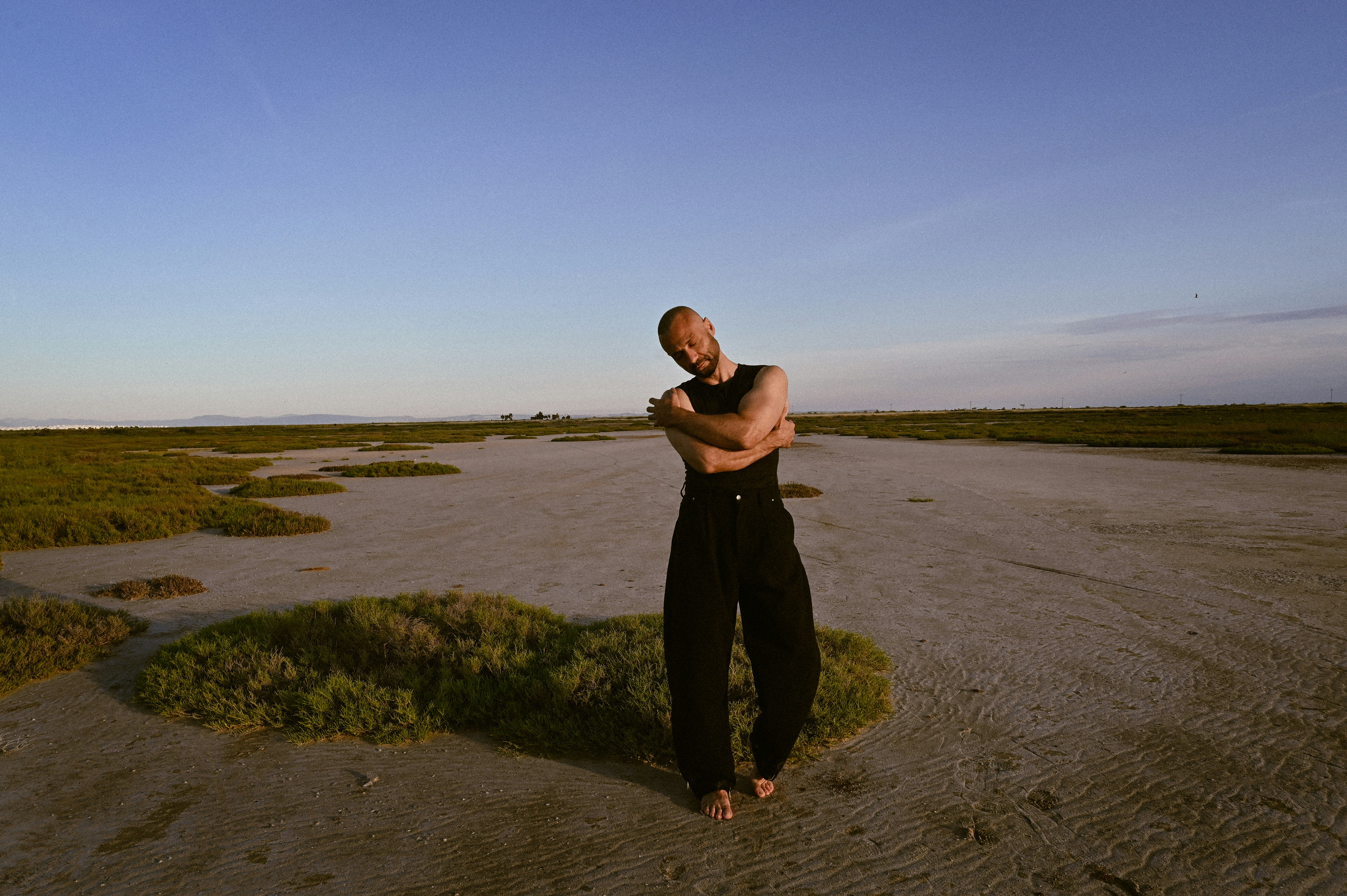 Arm-crossed silhouette at the edge of a salt flat at golden hour