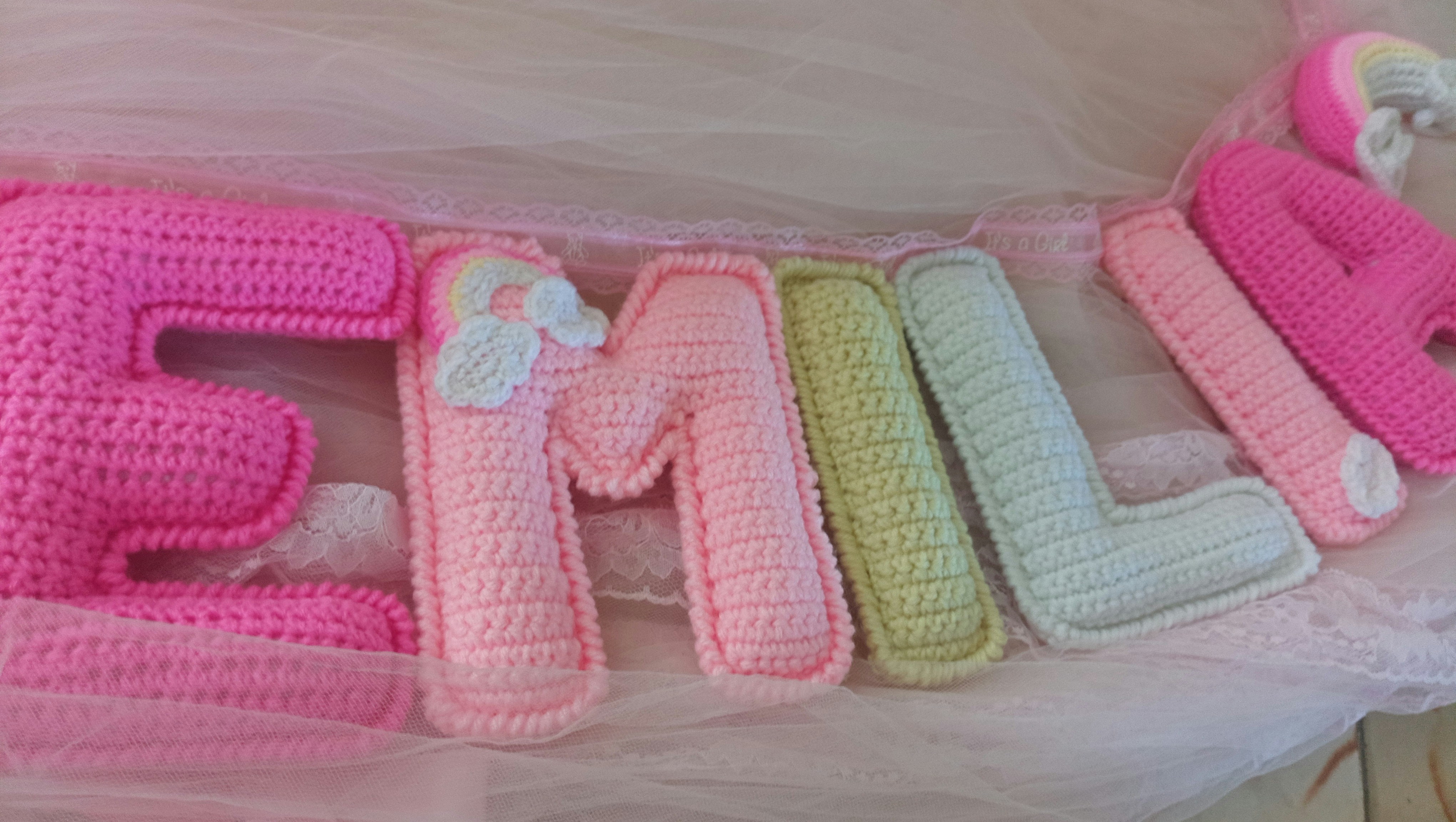 Crocheted pastel letters spelling 'EMILY' laid across soft tulle backdrop