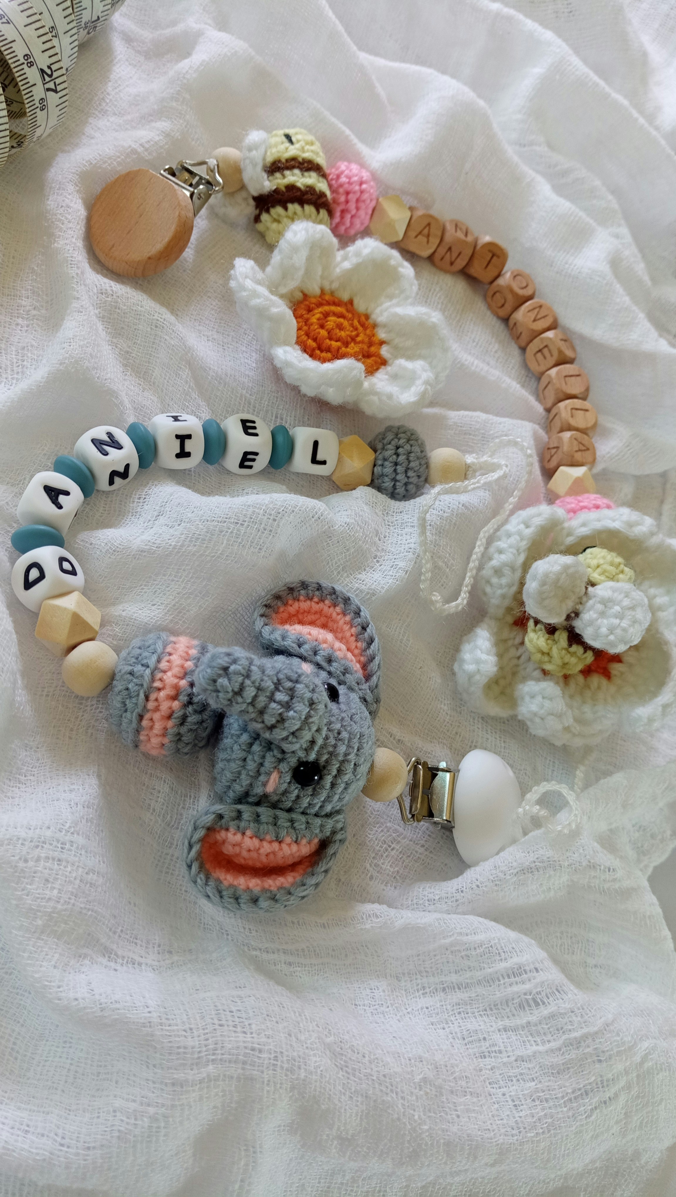 Handcrafted beaded pacifier clip with crocheted characters and wooden beads arranged on white fabric. A soft, cozy composition highlighting texture and color of the toys.