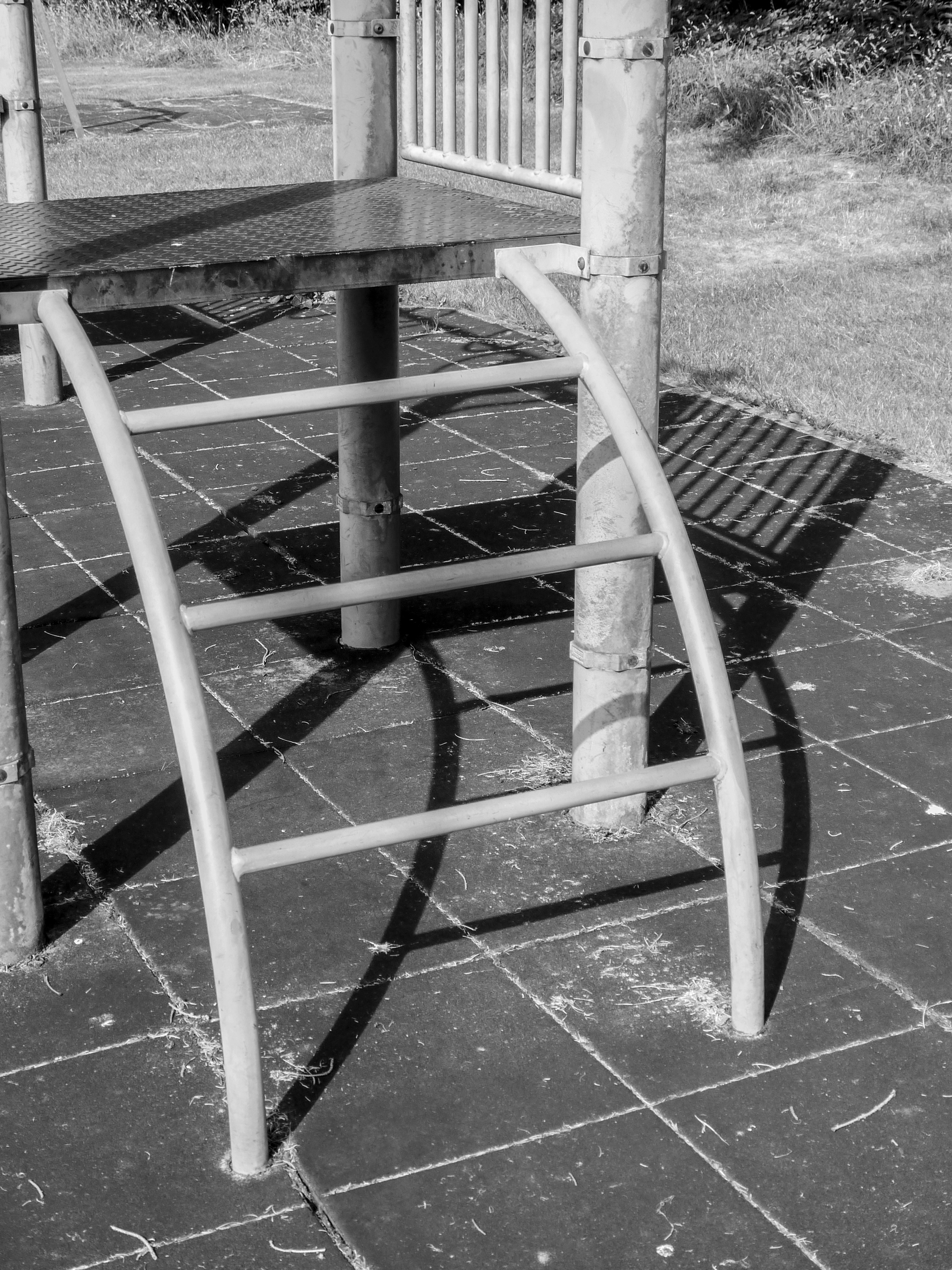 Shadows on the playground stairs: a metal ladder crowned by the sun