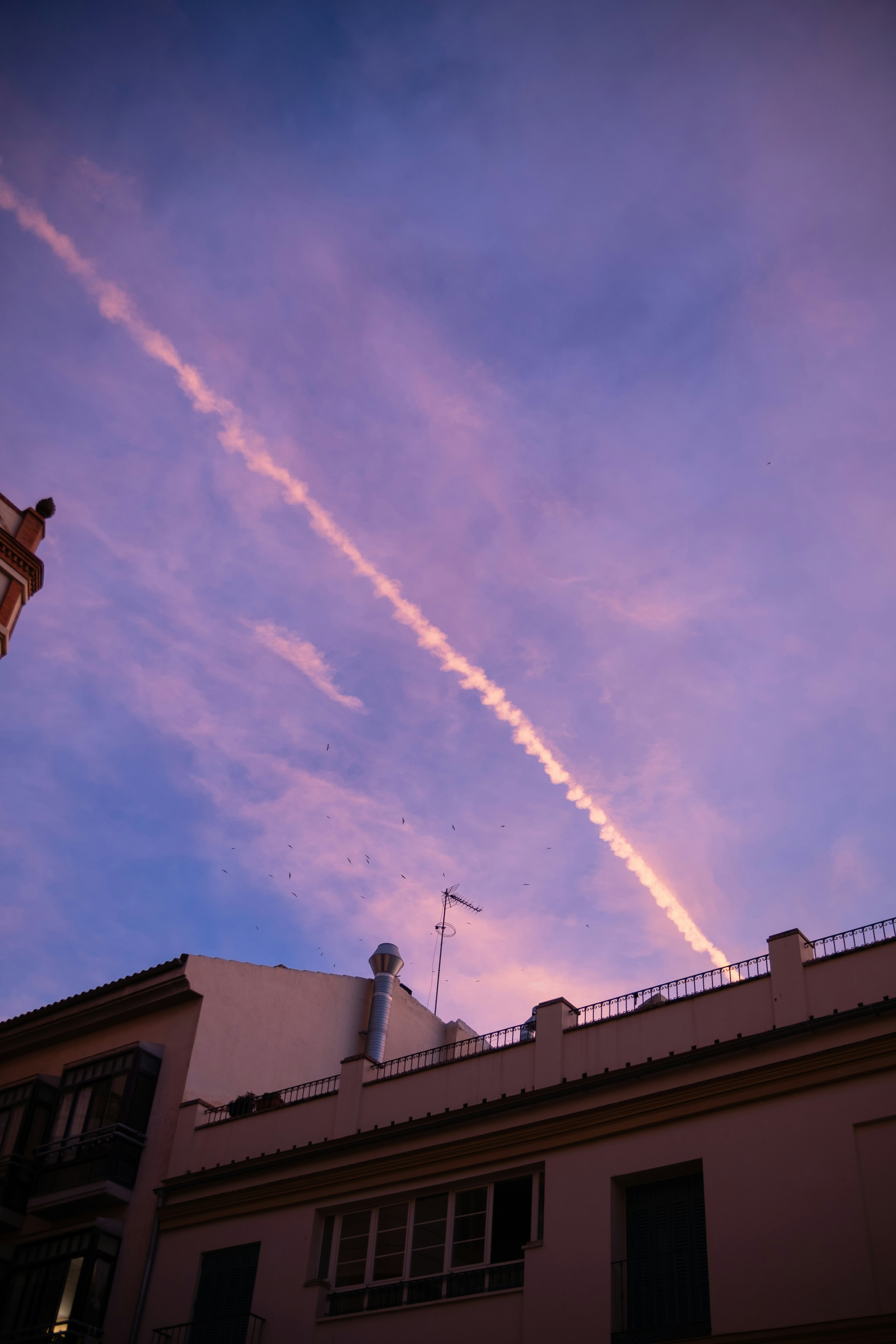 Soft pink-tinged sky with a diagonal contrail above the rooftop silhouettes, suggesting late-day urban calm.