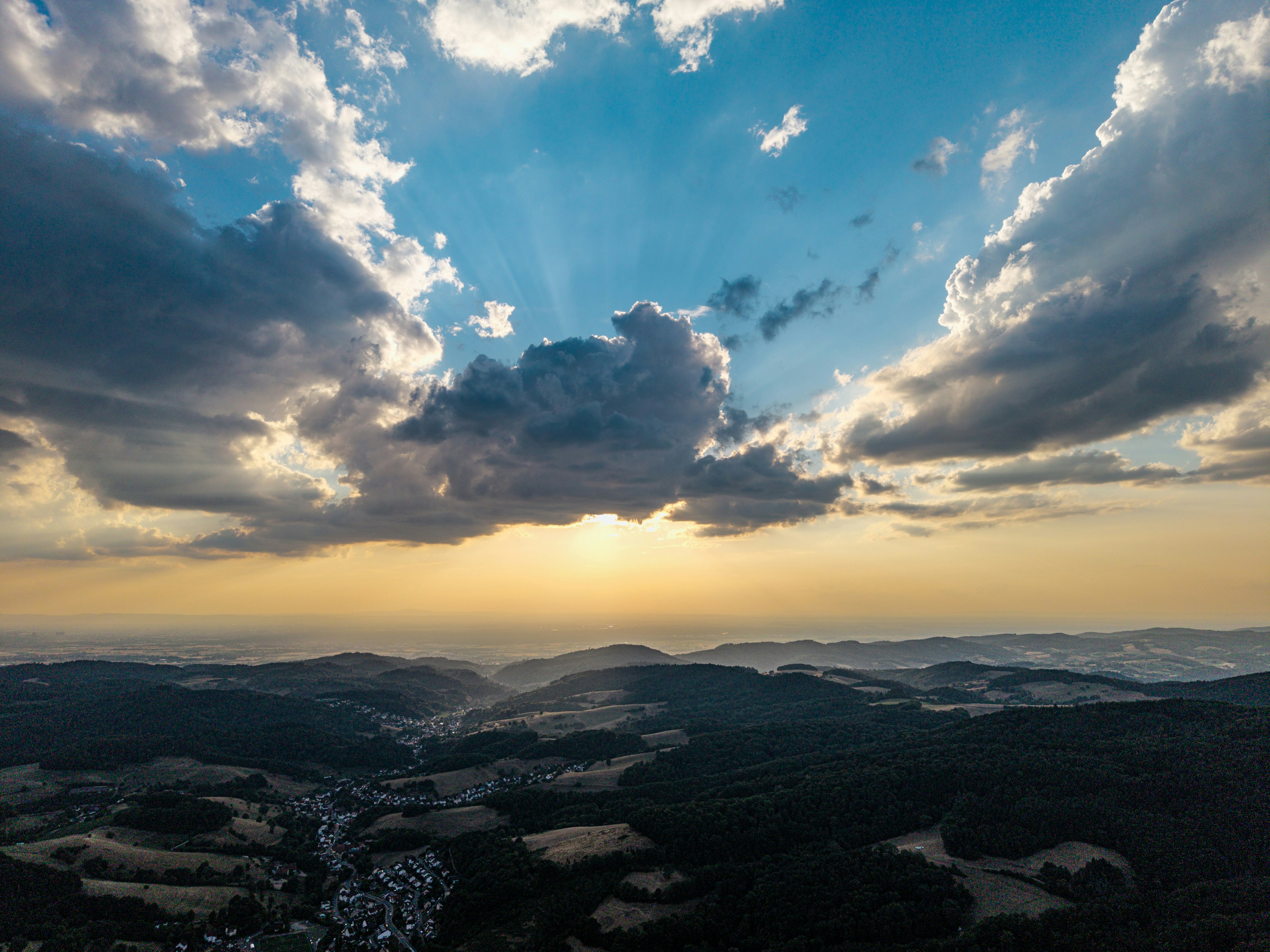 Sunlit Ridge: Distant Village Beneath a Sky of Piercing Ray Creases