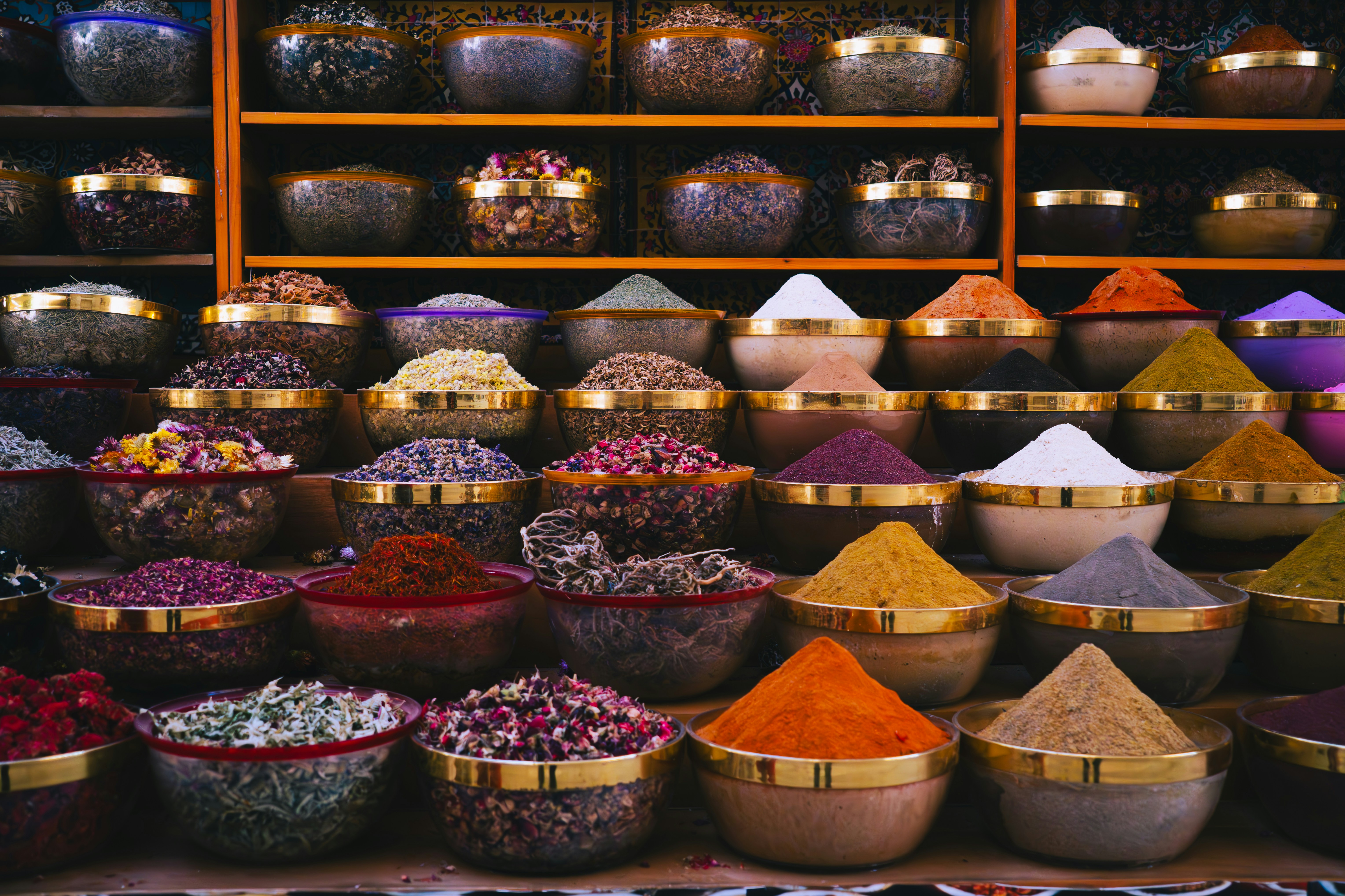 Vibrant display of aromatic spices, dried herbs, and colorful floral teas in market bowls.