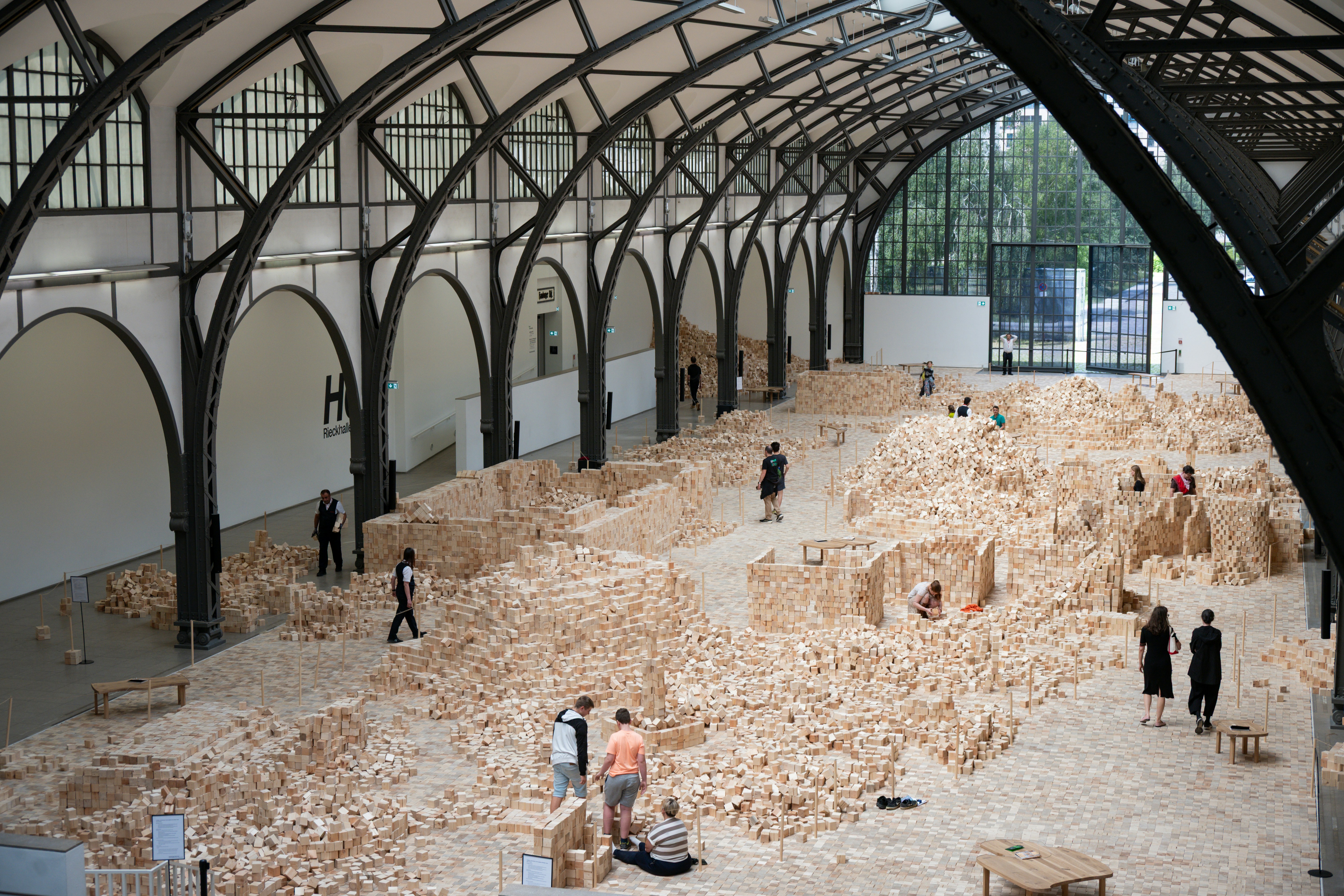 People walking through a large hall filled with wooden blocks.