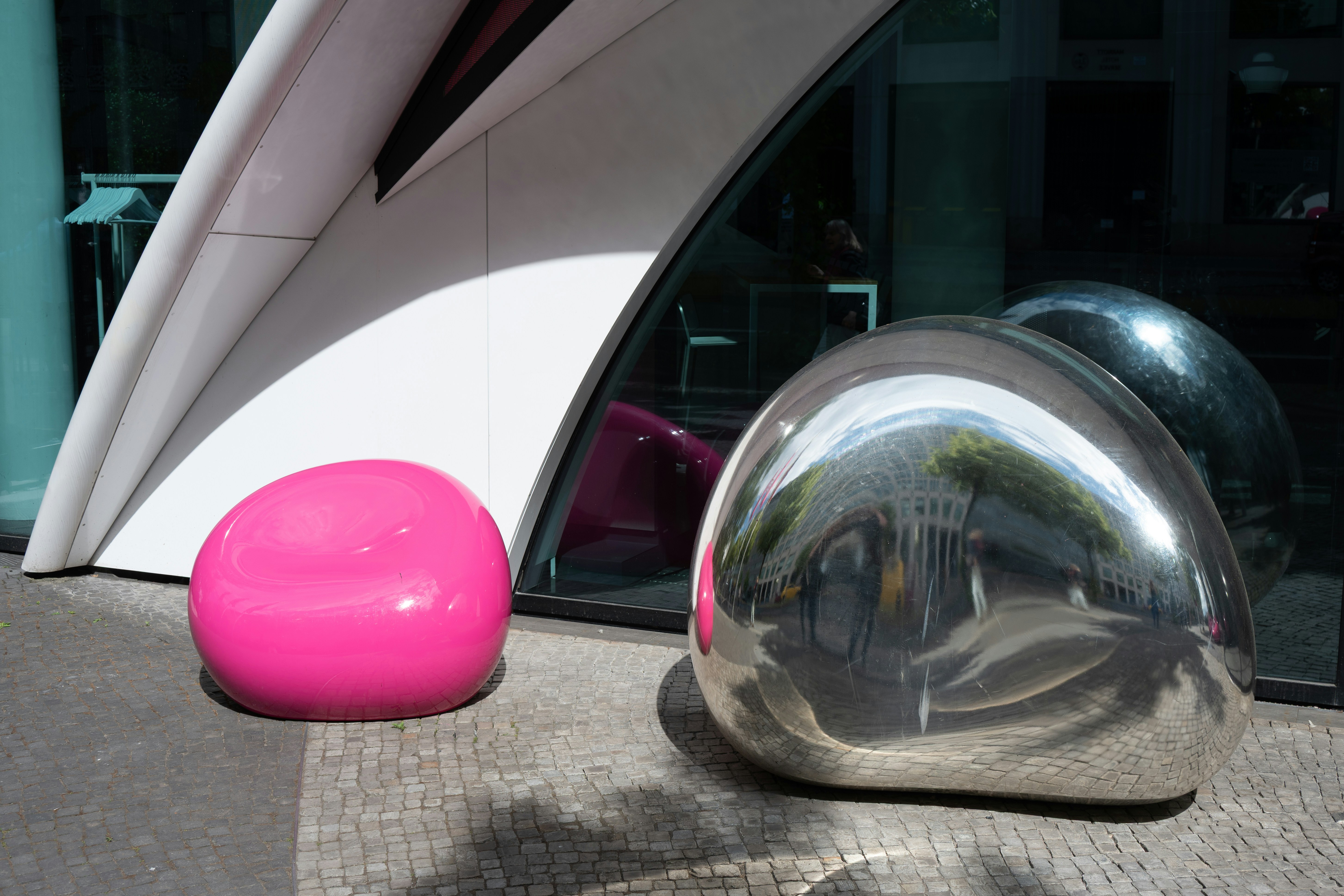 Polished stainless spheres and a glossy pink pebble at a modern facade